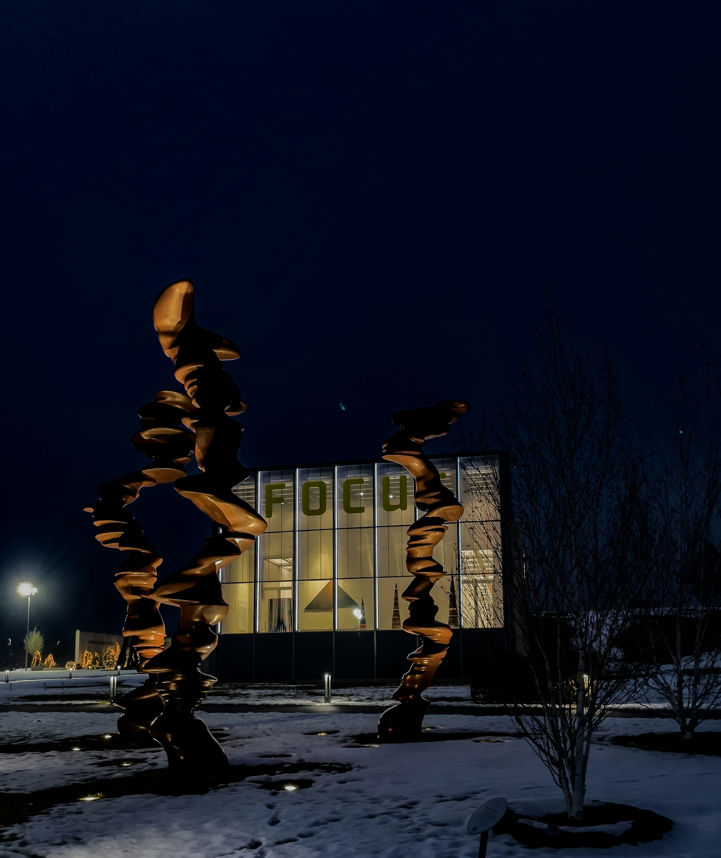 Illuminated Forum: Two twisting sculptures framing a glowing glass-fronted building