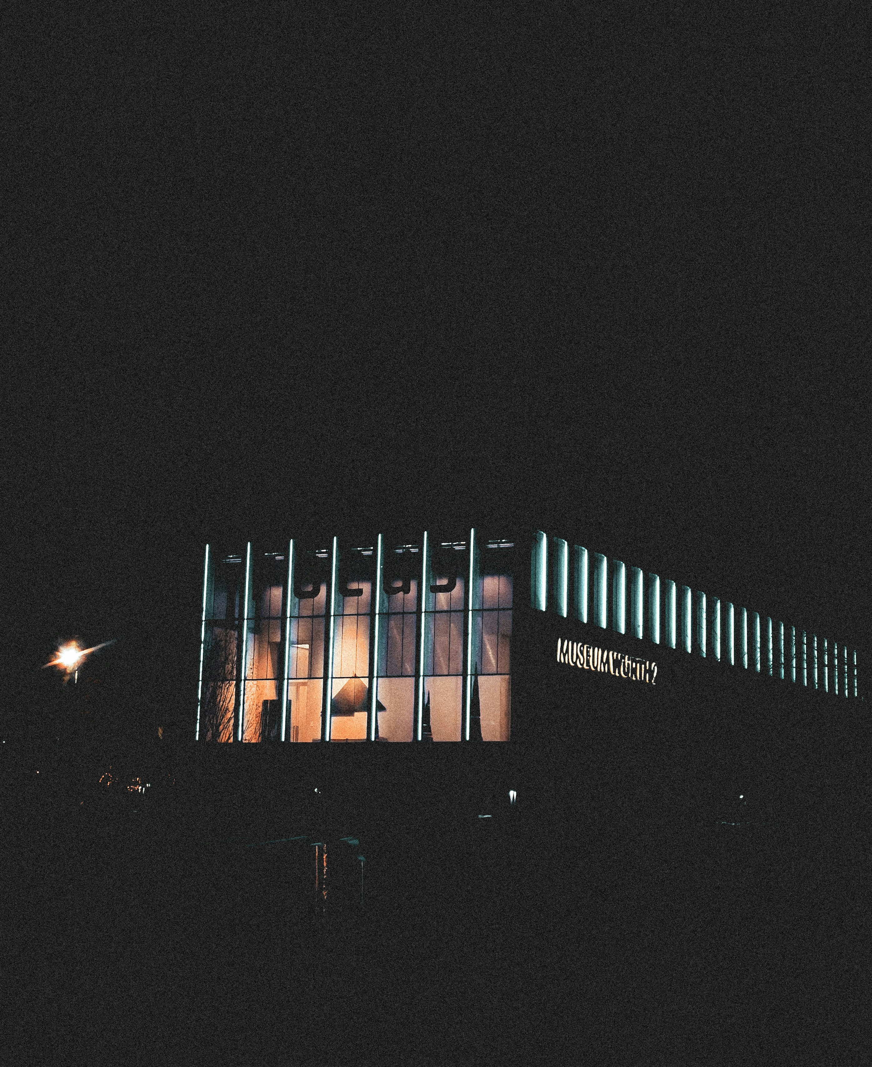 Night Glass: museum facade lit in aqua and amber beneath a starless sky