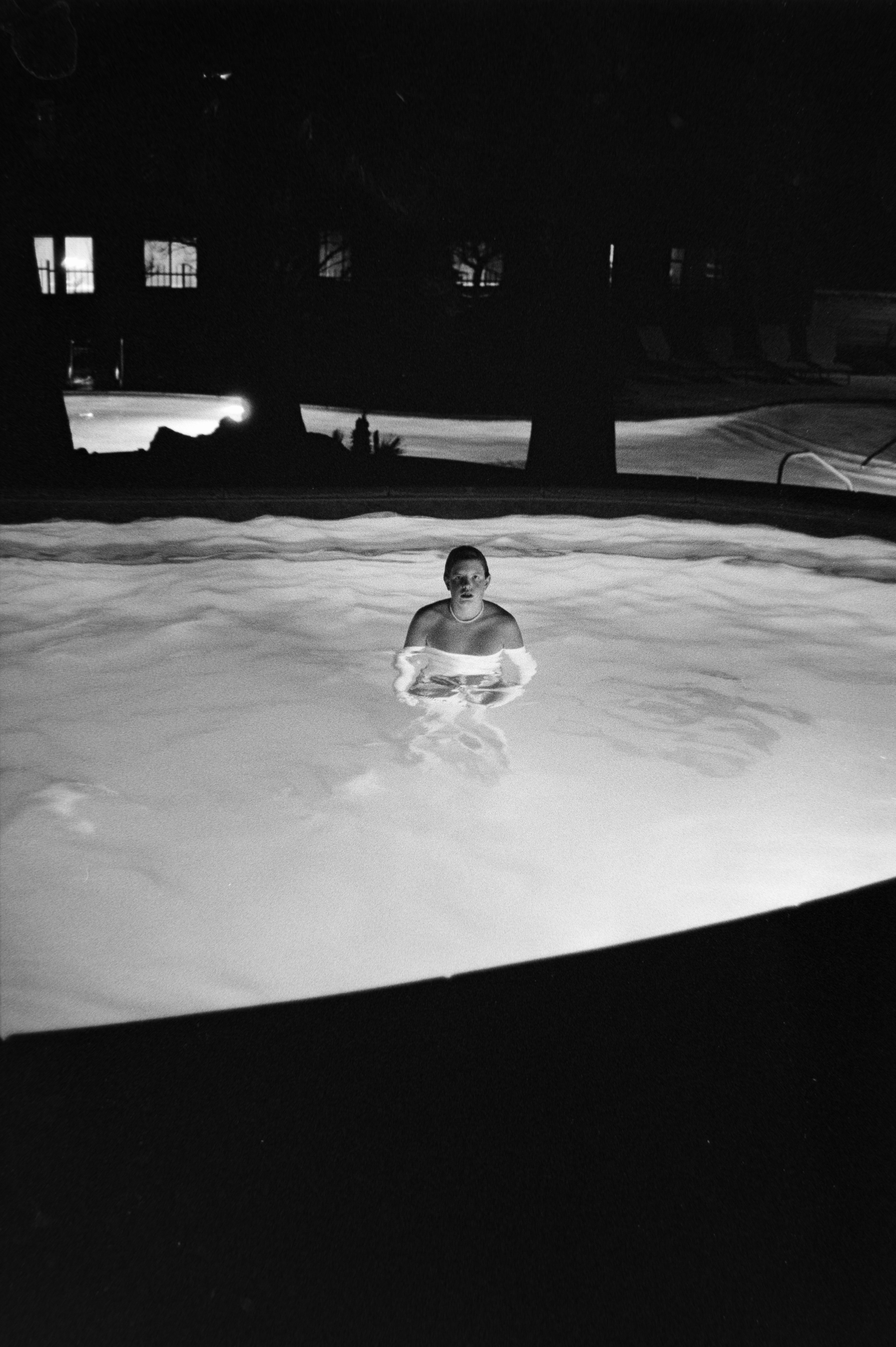 Floating Night: A Quiet Figure in a Pool Under Moonlit Shadows