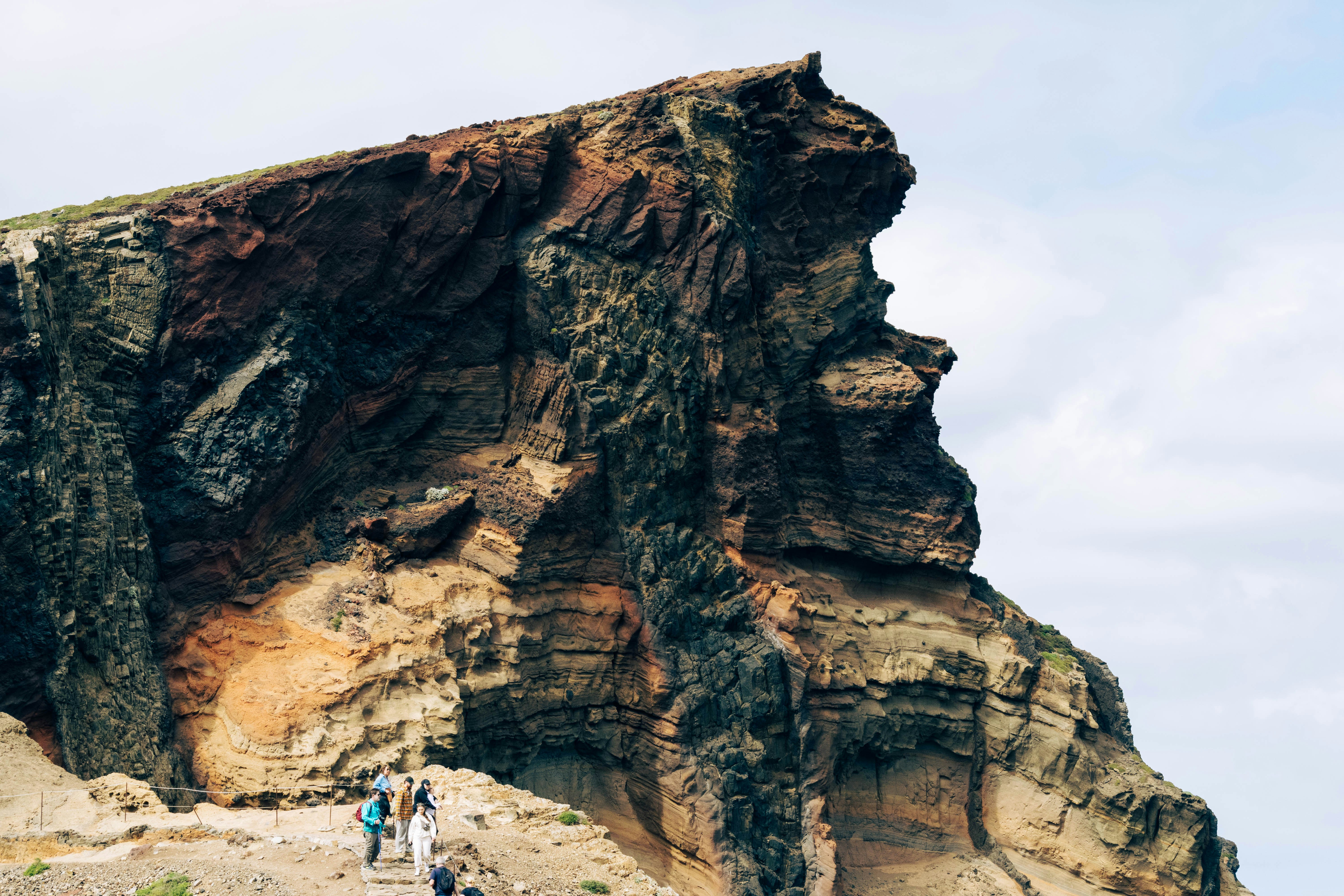 Trail to the basalt cliff: hikers at the base of a rugged coastal outcrop