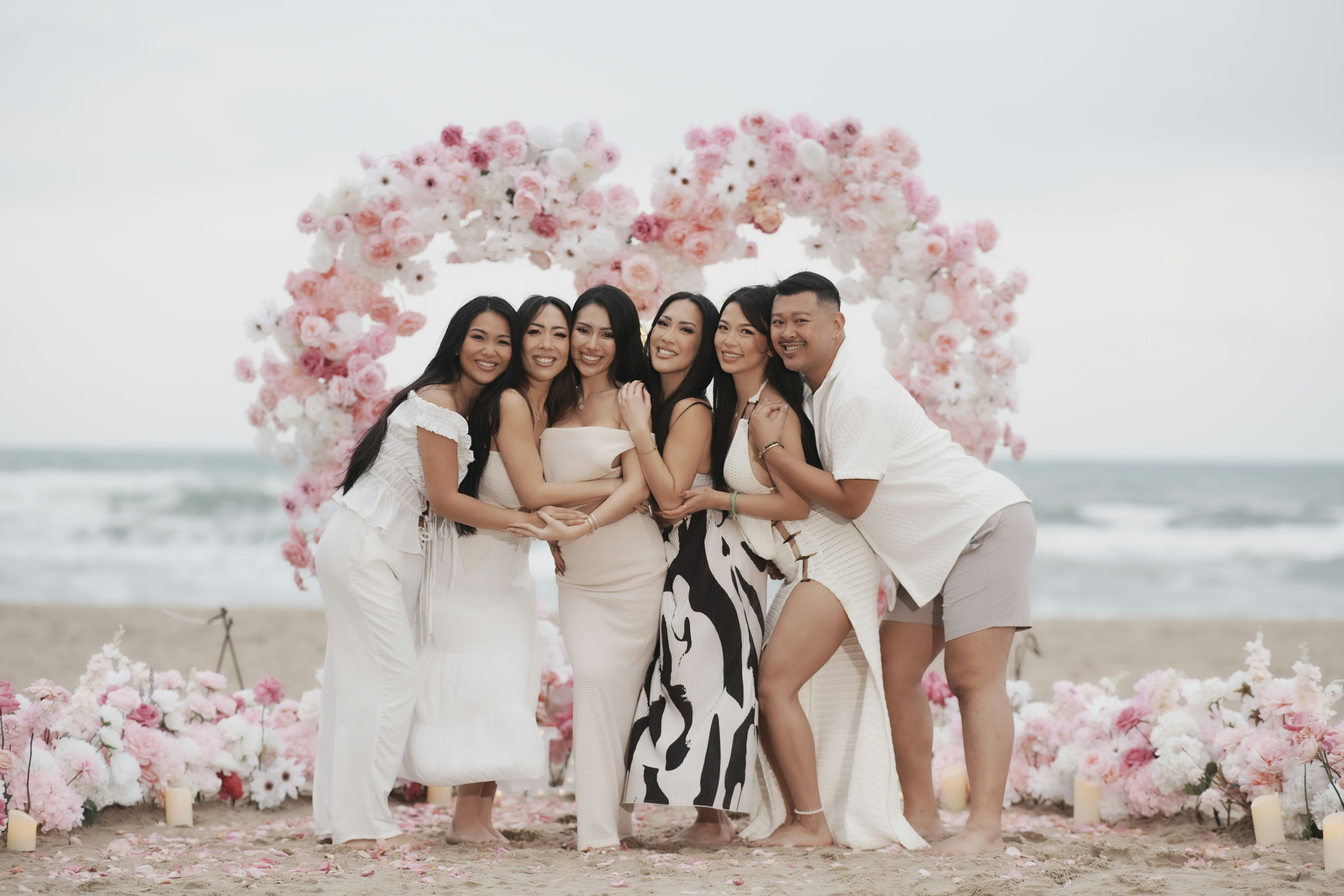 Heartfelt Circle: A Wedding Party Framed by Blossoms on the Beach