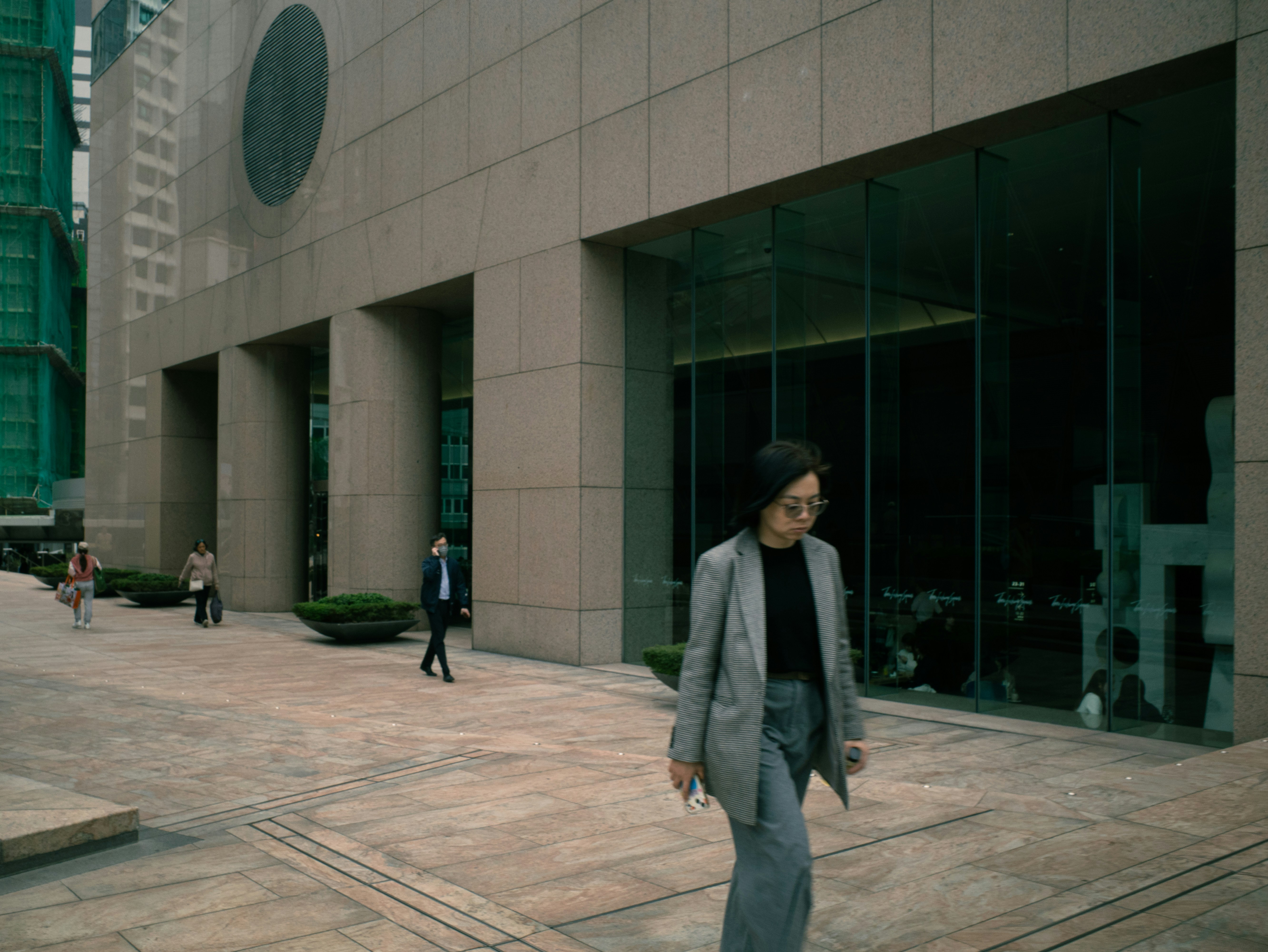 City Street Portrait: Woman in Light Gray Coat Steps Through Modern Architecture