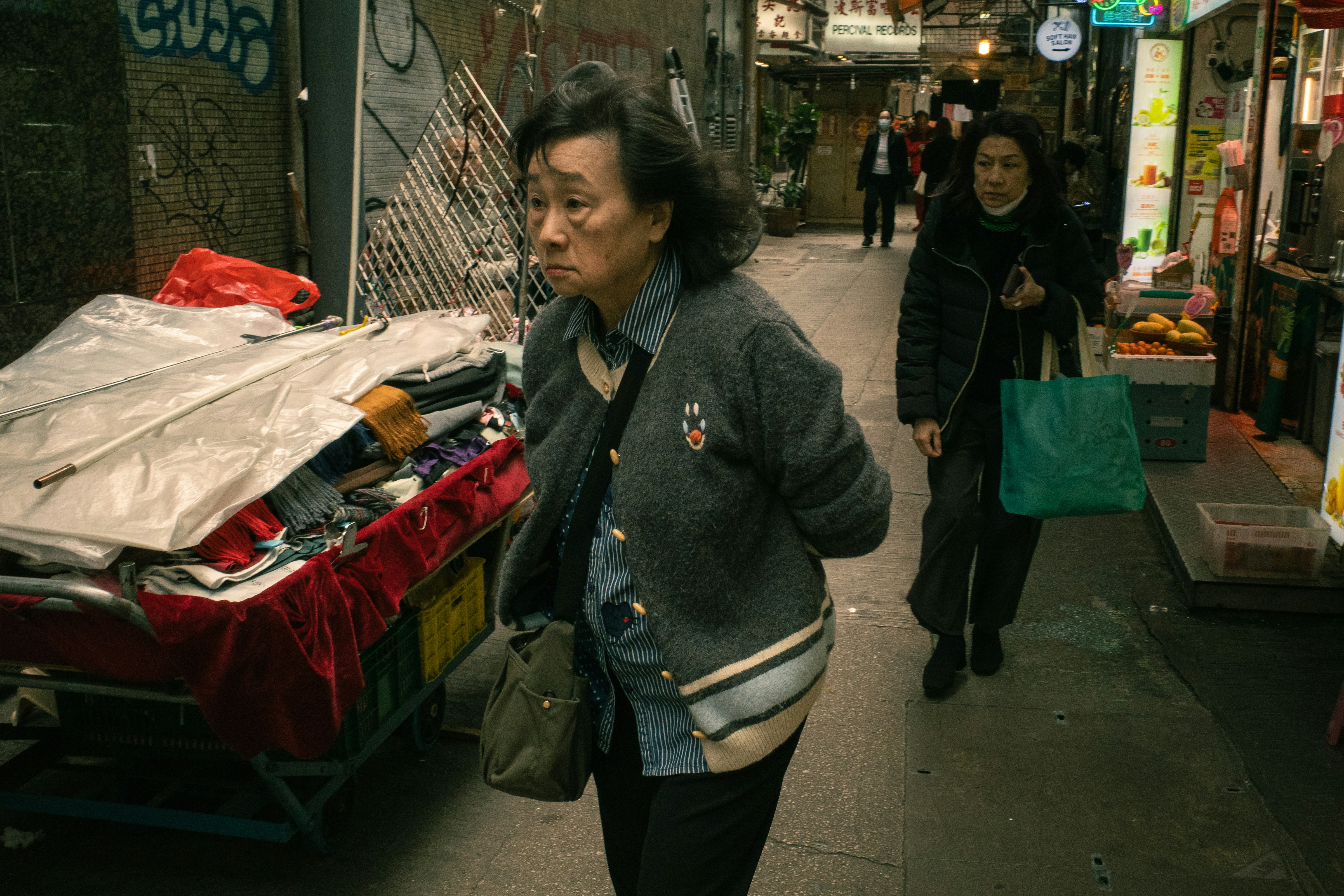 Street Portrait: A Senior Woman Leads the Quiet Walk Through a Market Alley