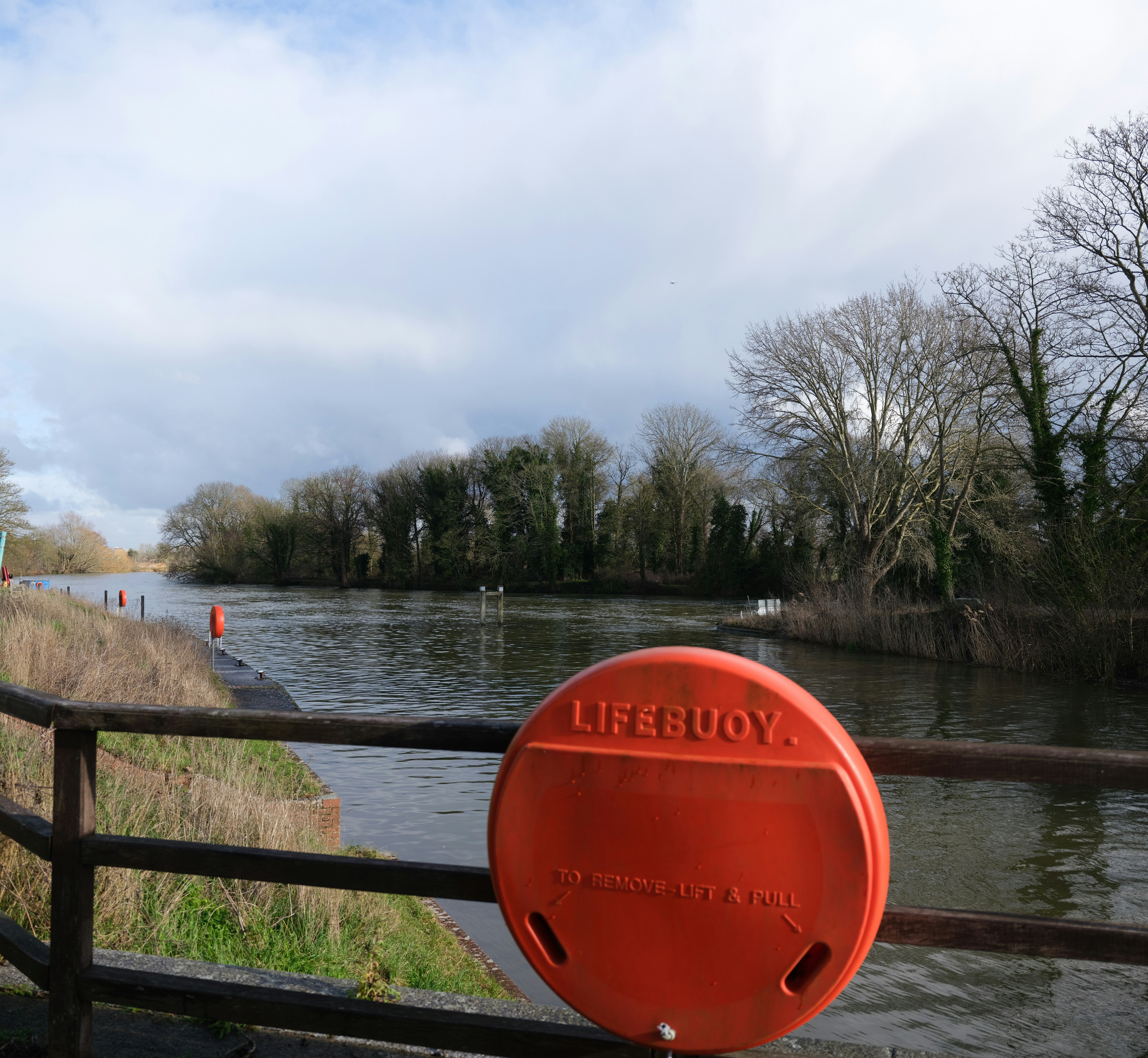 Red Lifebuoy on a Riverside Fence Beckons from a Quiet Channel