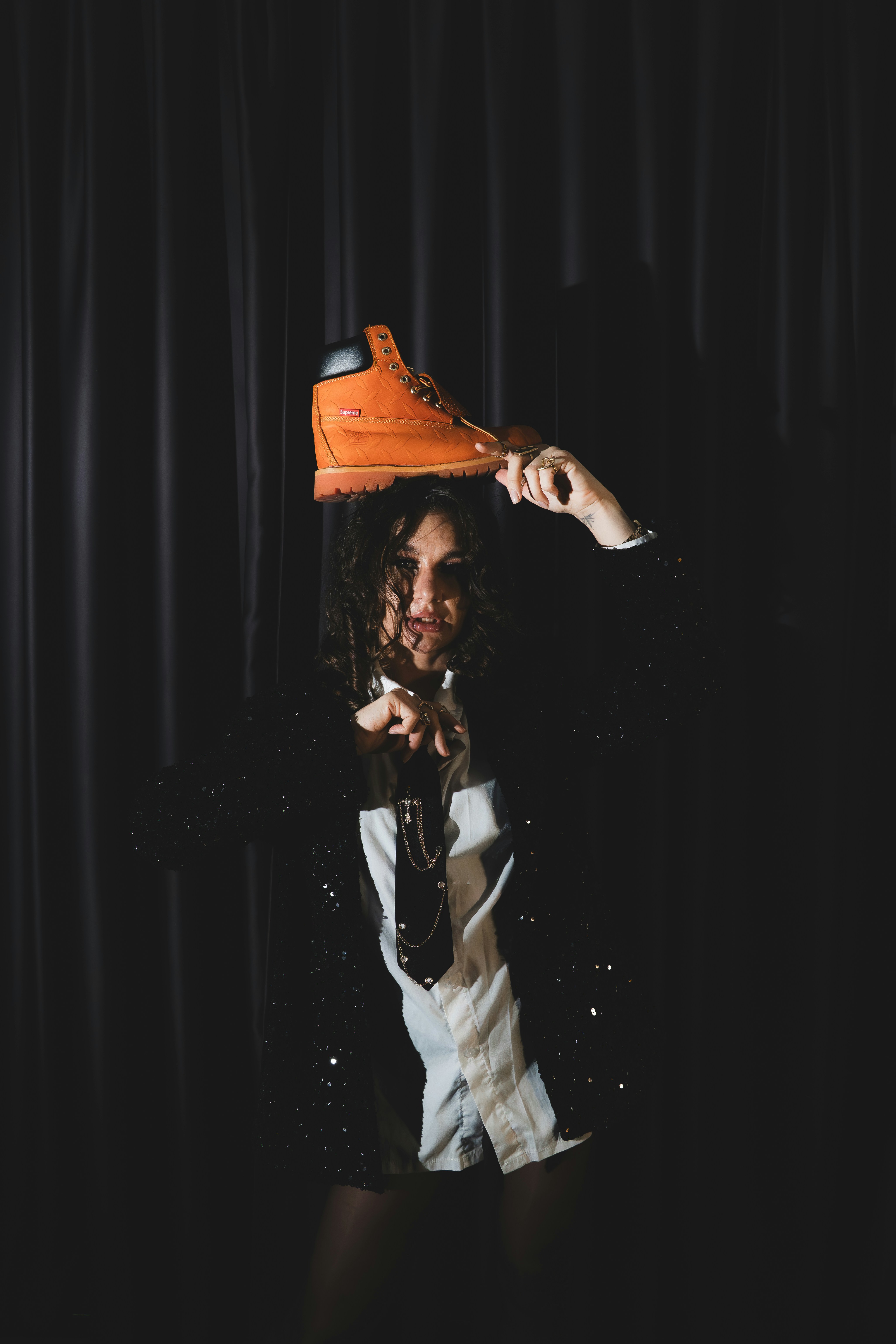 An Orange Pivot: Footwear Raised Above a Dressed Figure in a Dark Studio