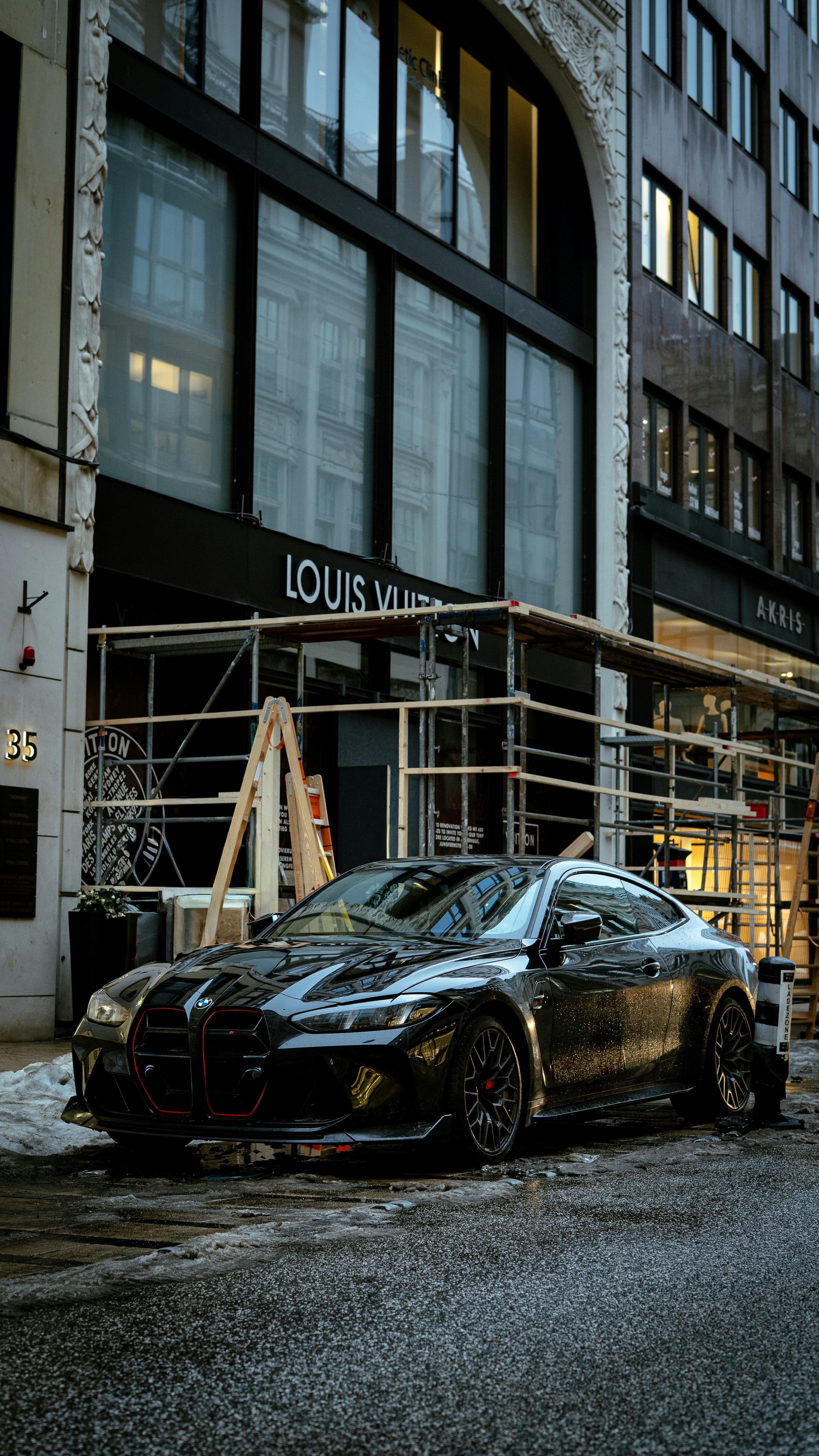 Glossy black supercar under urban restoration on a rain-slicked street