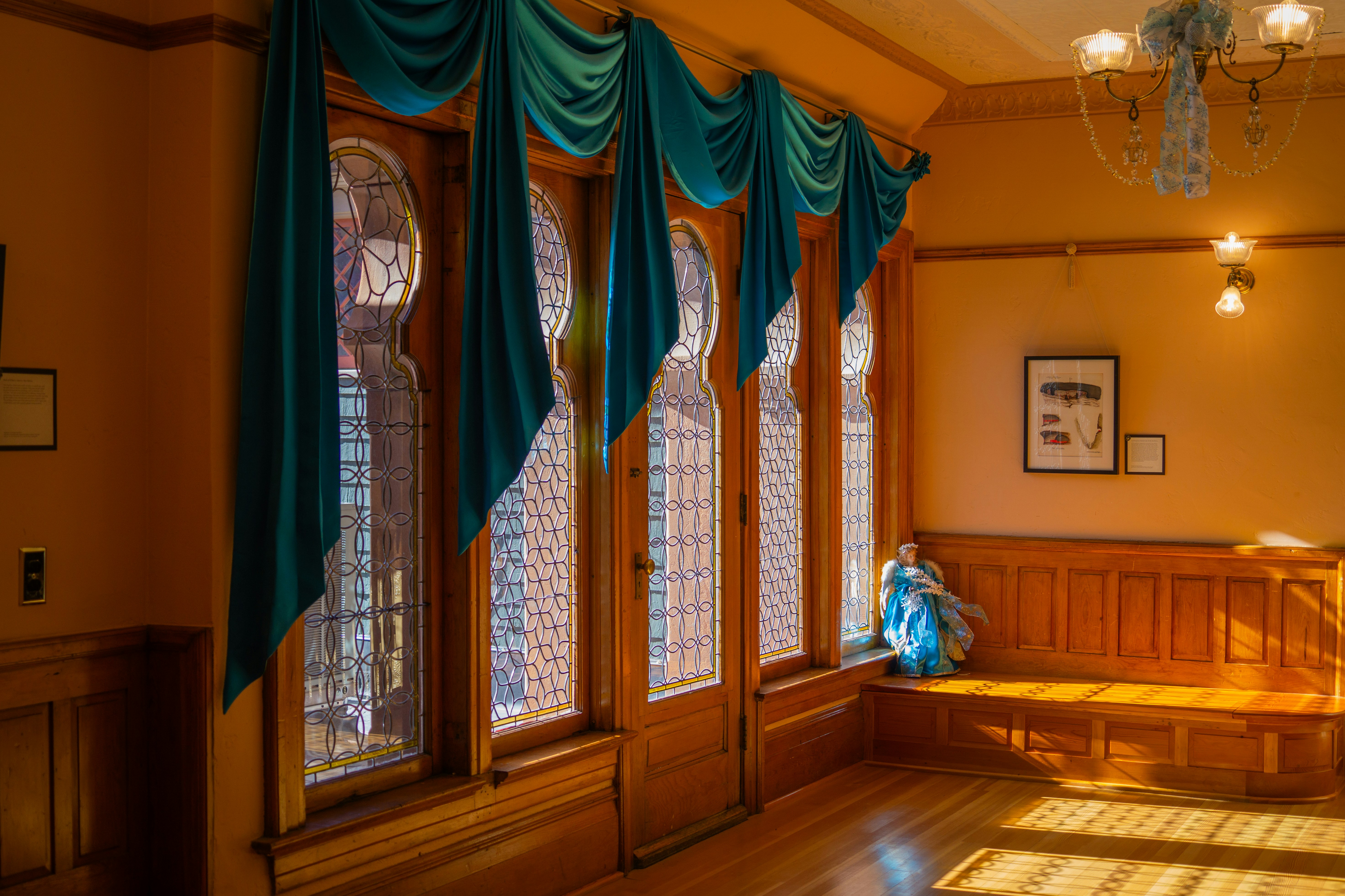 Sunlit corner with teal drapes and a small doll on the wooden bench