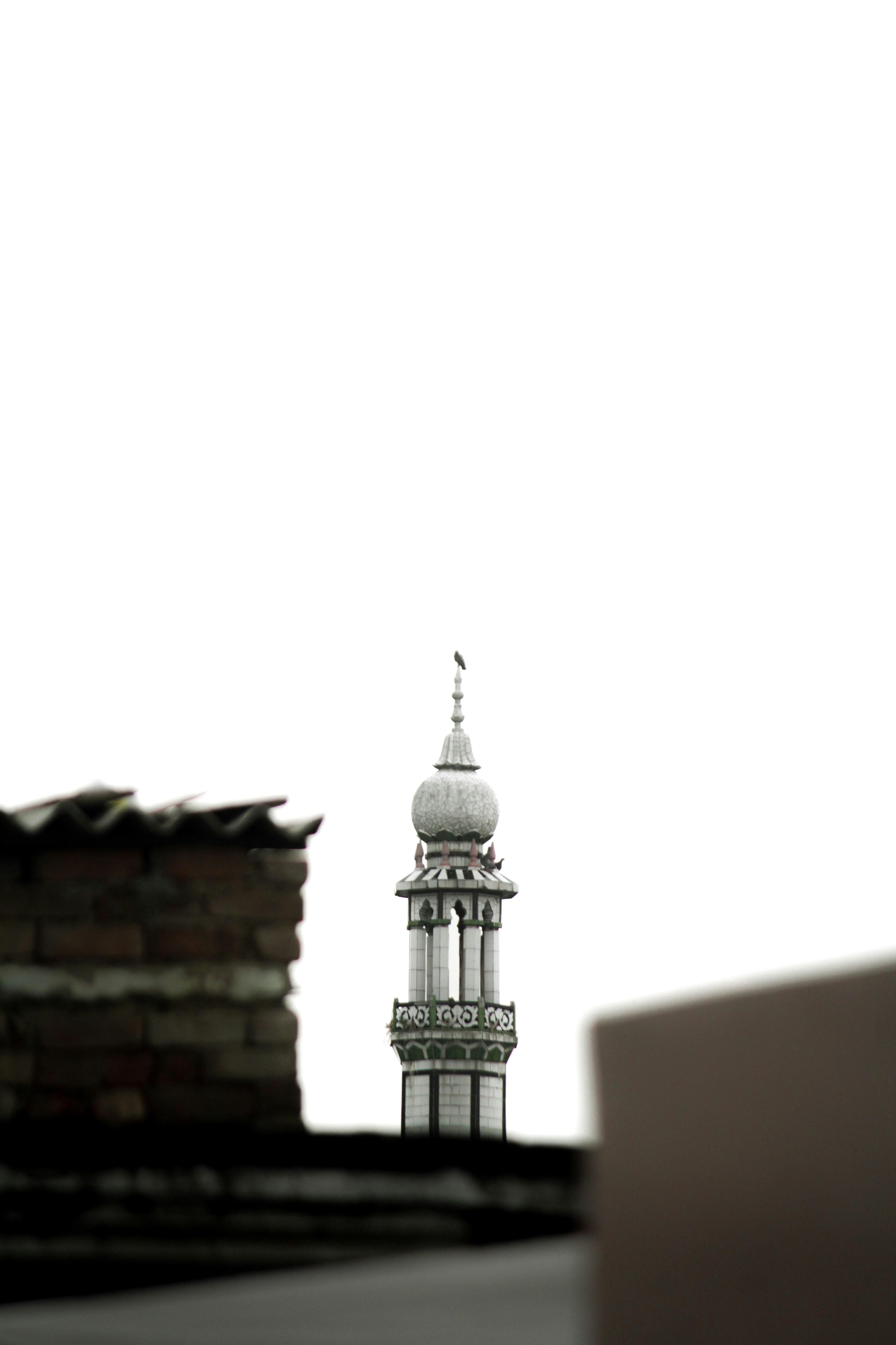Spire Amid White Sky: A Rooftop Moment with a Slim Minaret