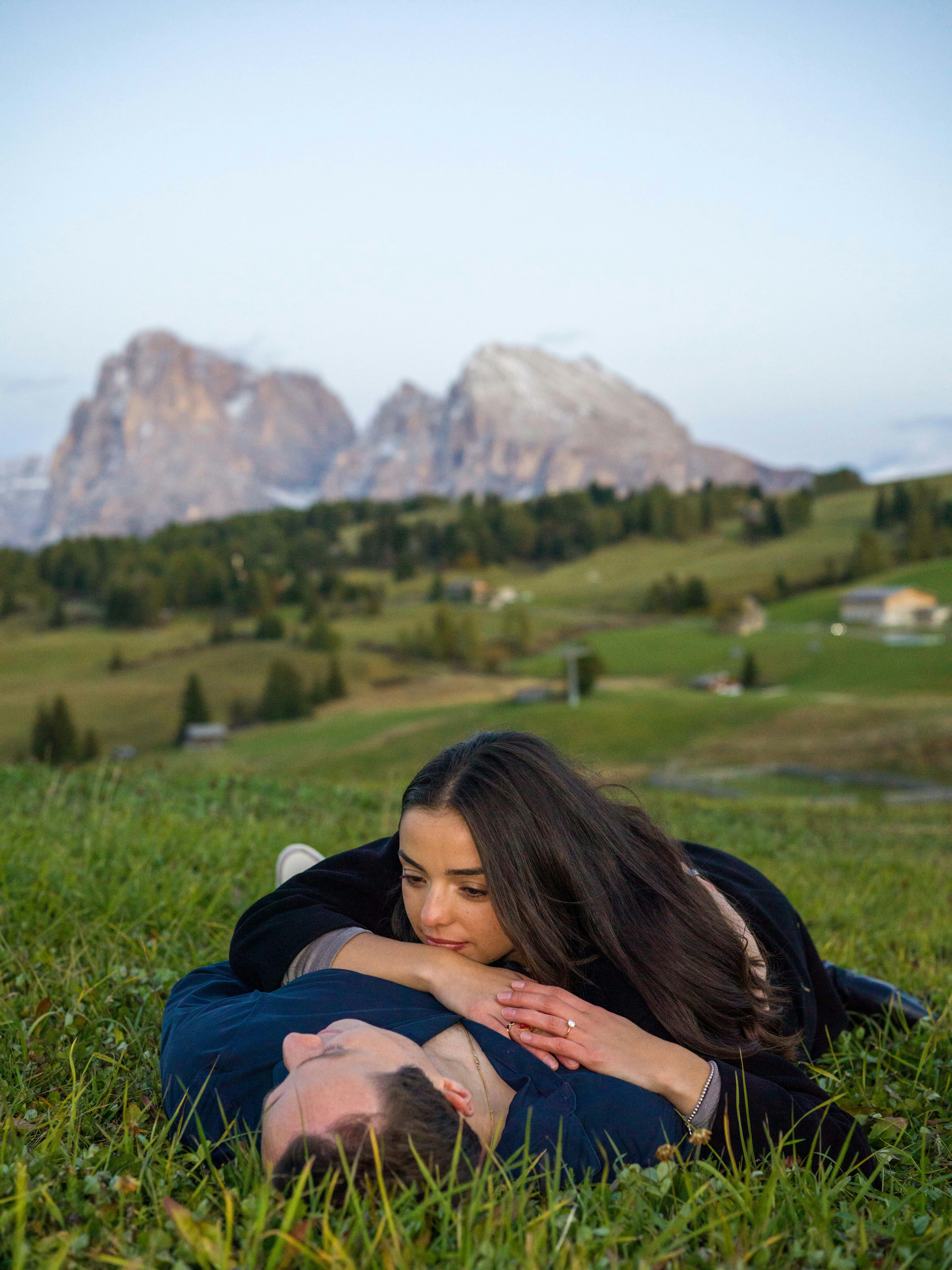 Field of Quiet: Couple Resting Amid Rolling Hills Under Mountain Skies