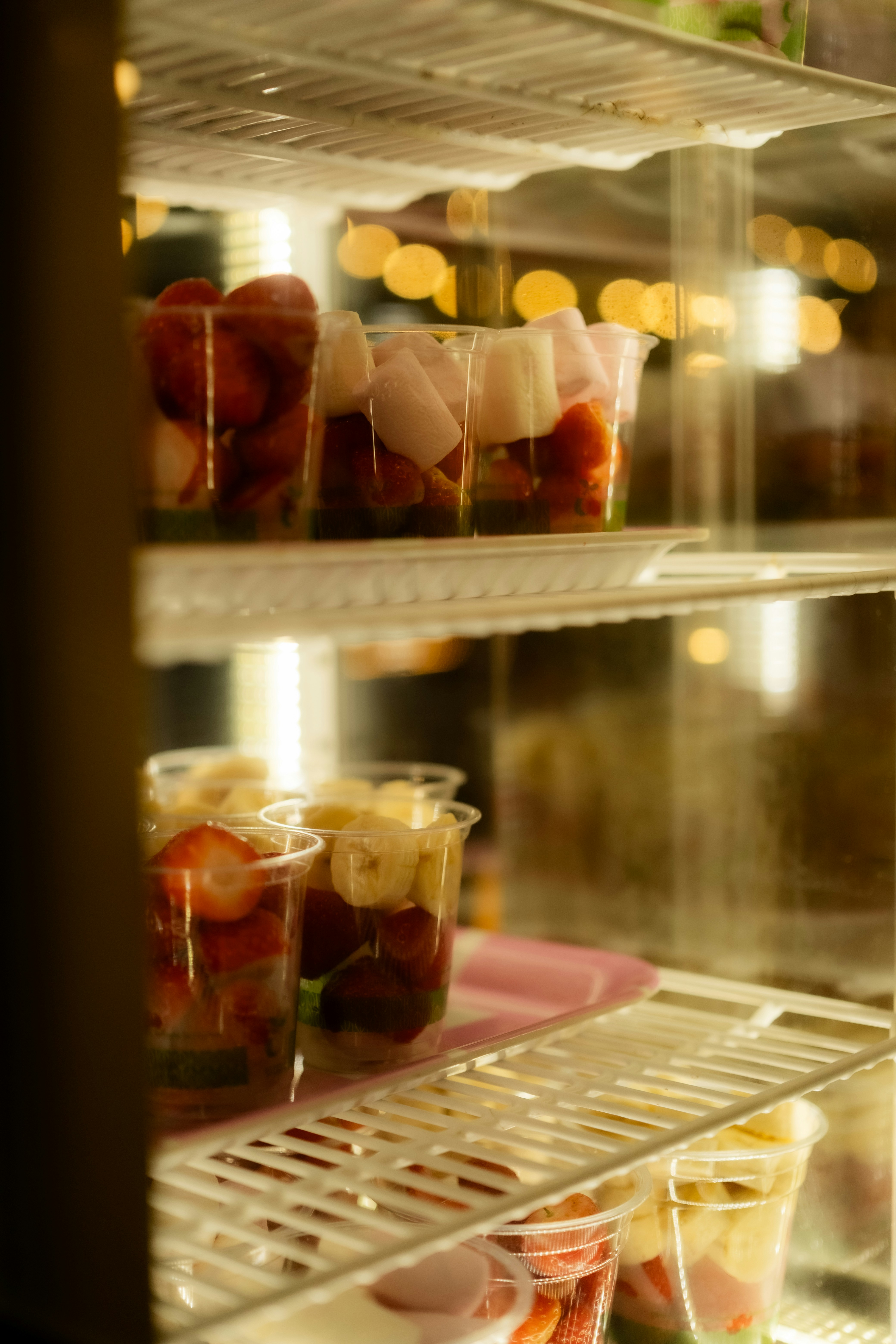Fruity dessert cups behind a refrigerated shelf glow