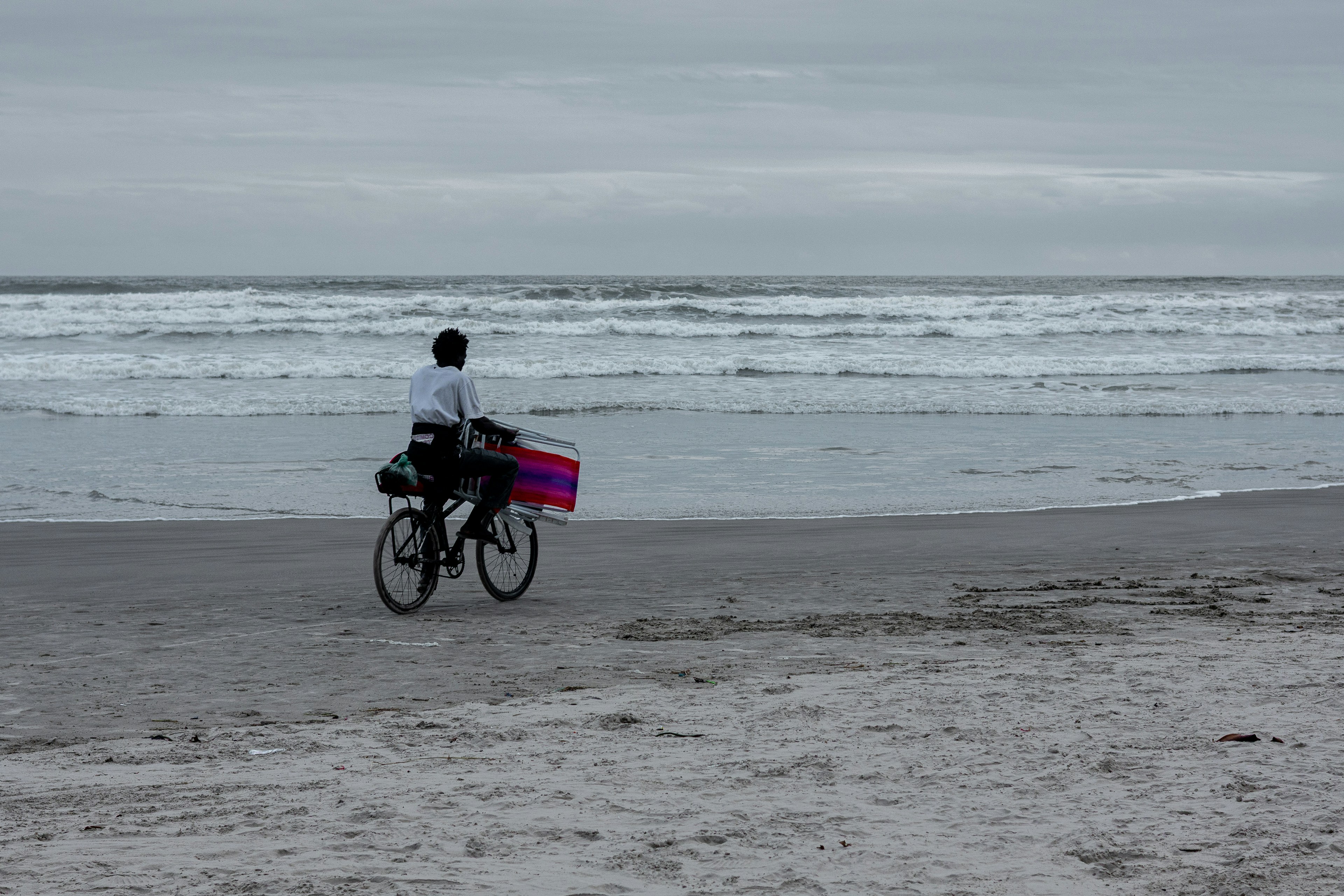 Cyclist on a Quiet Beach with a Pride Flag in Tow