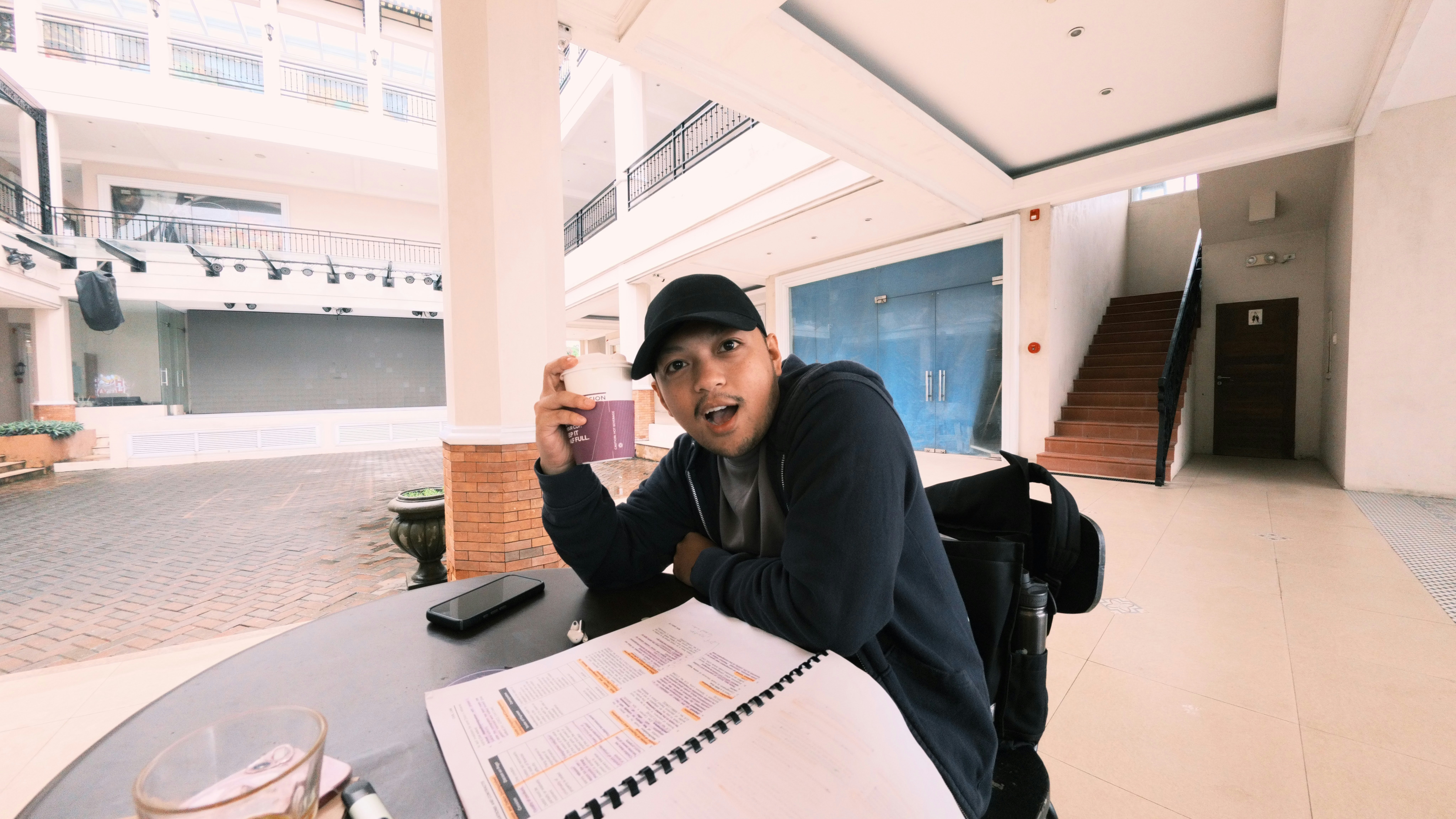 Man with cap holding drink at table with papers