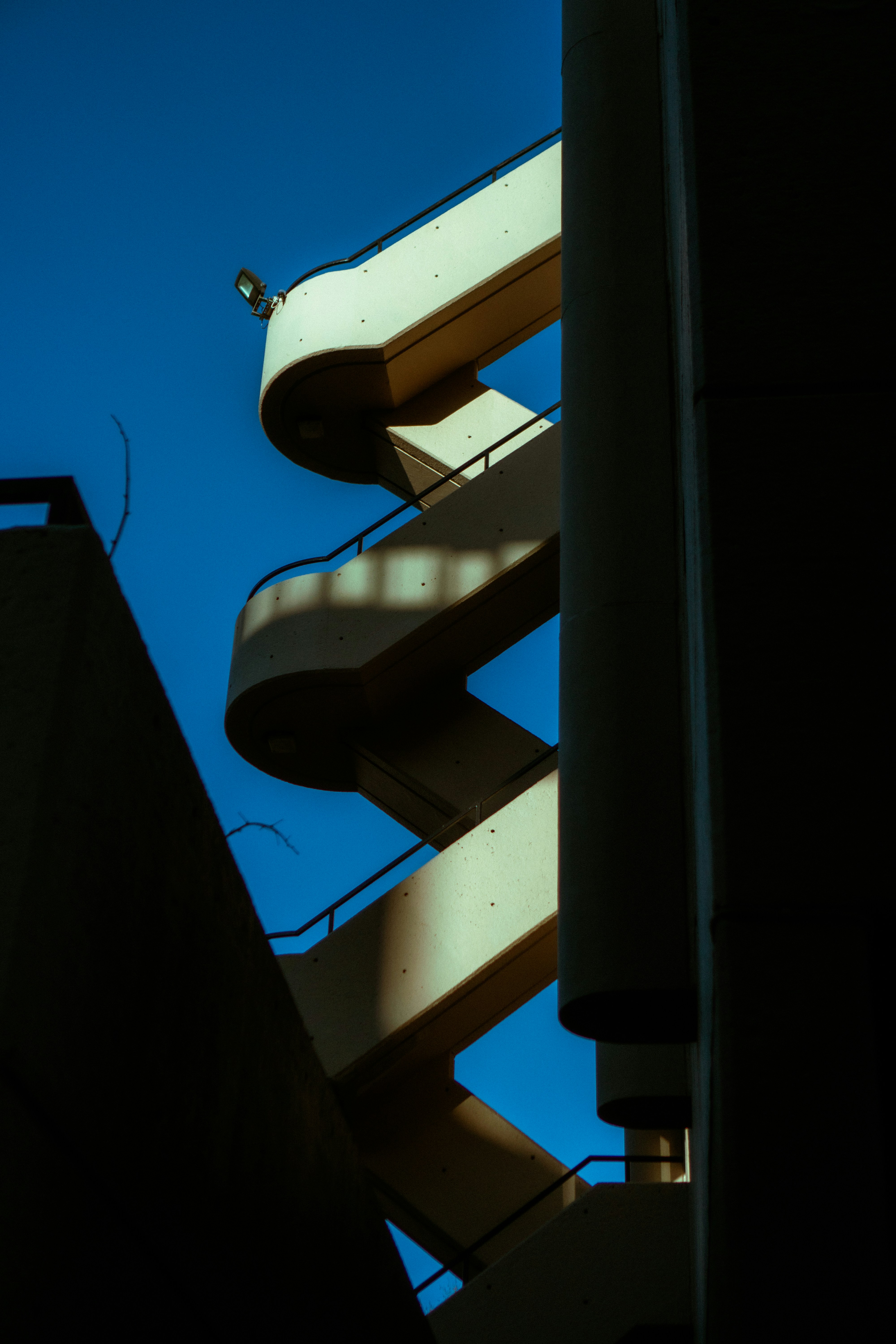 Blue Staircase to the Sky: Concrete Curves Against a Sharp Shadowed Facade