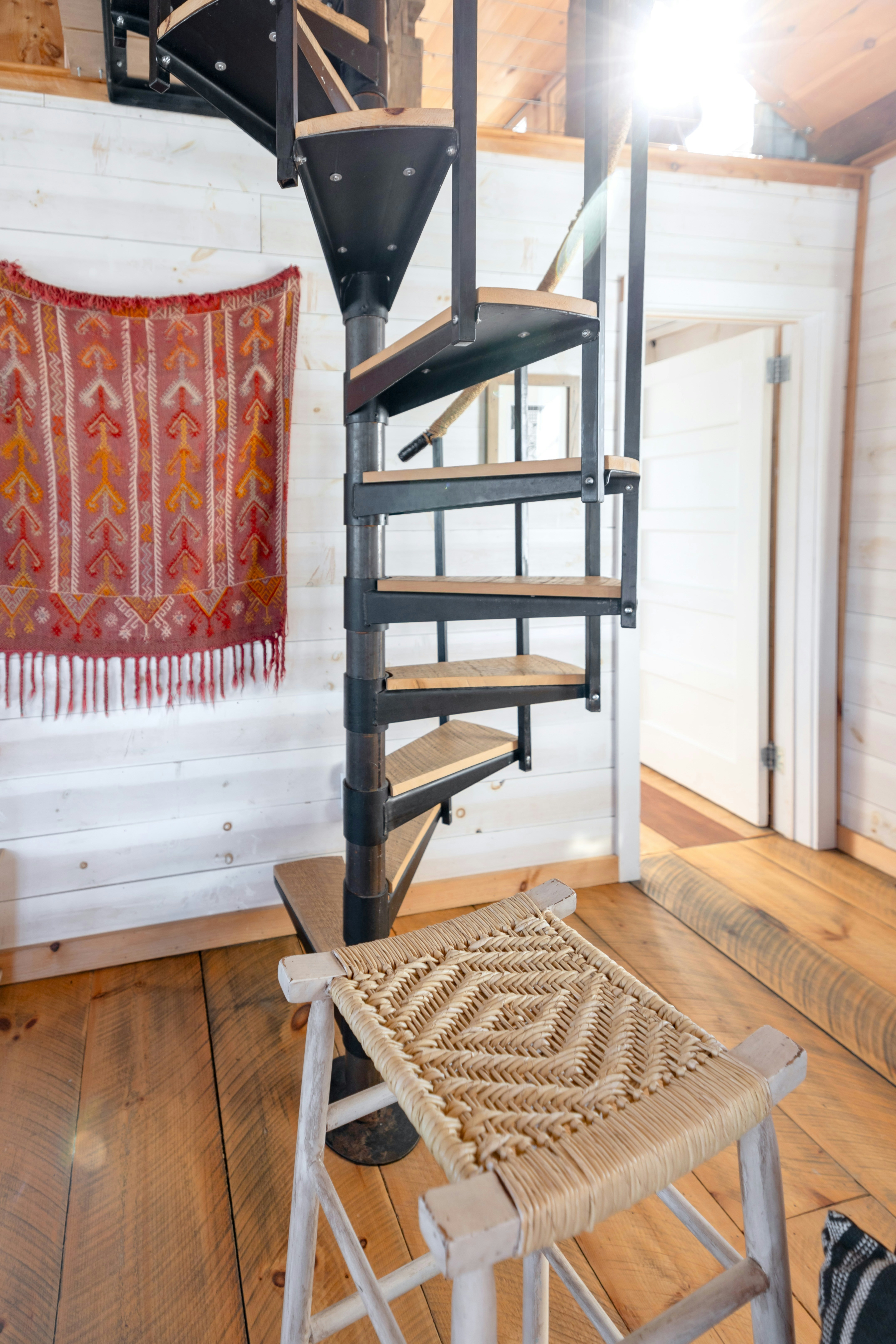Spiral Staircase and Woven Stool in a Sunlit Cabin Hall