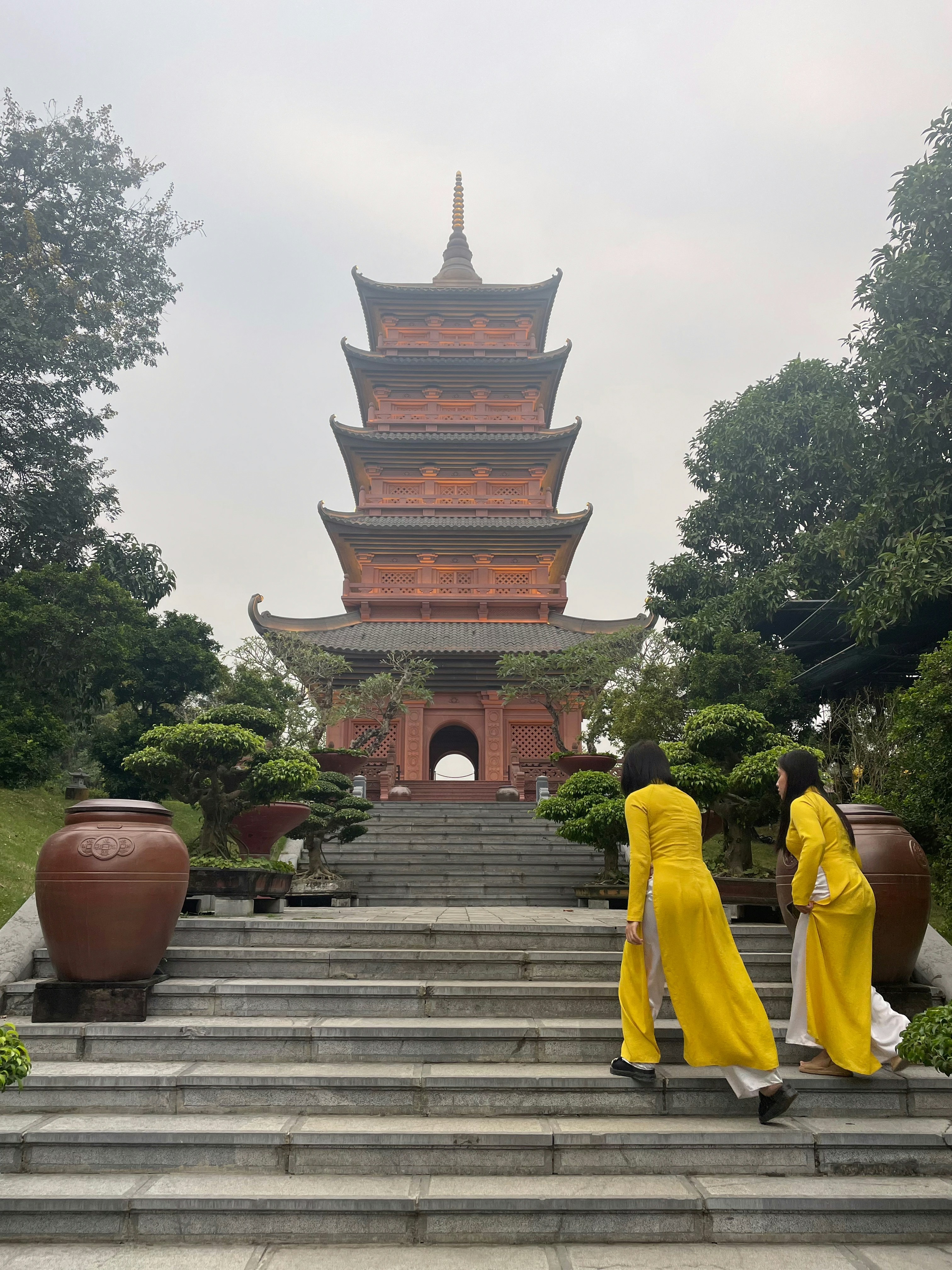Yellow-robed pilgrims ascend toward a multi-tiered pagoda in a tranquil temple setting