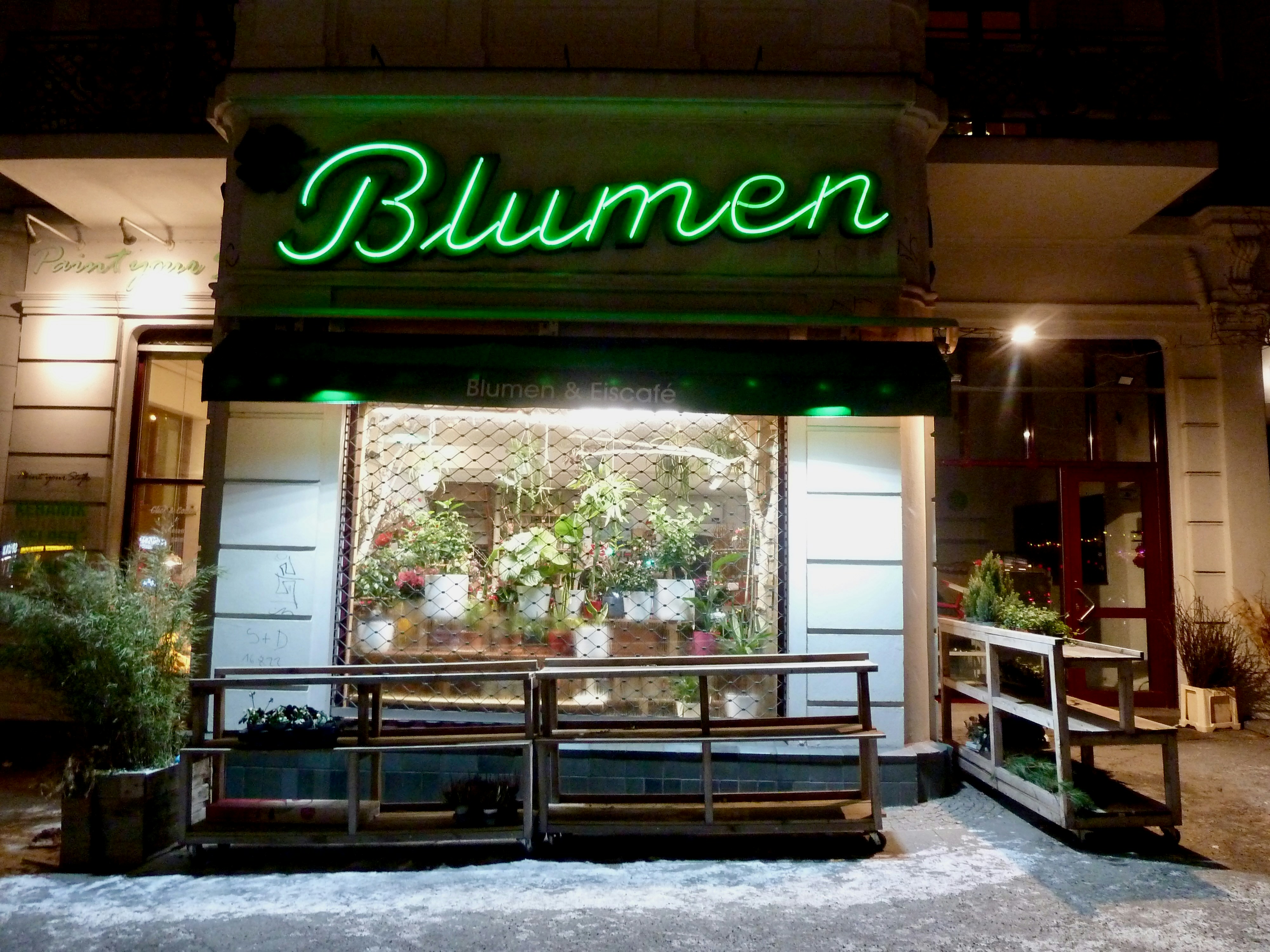 A storefront with a neon "blumen" sign at night.
