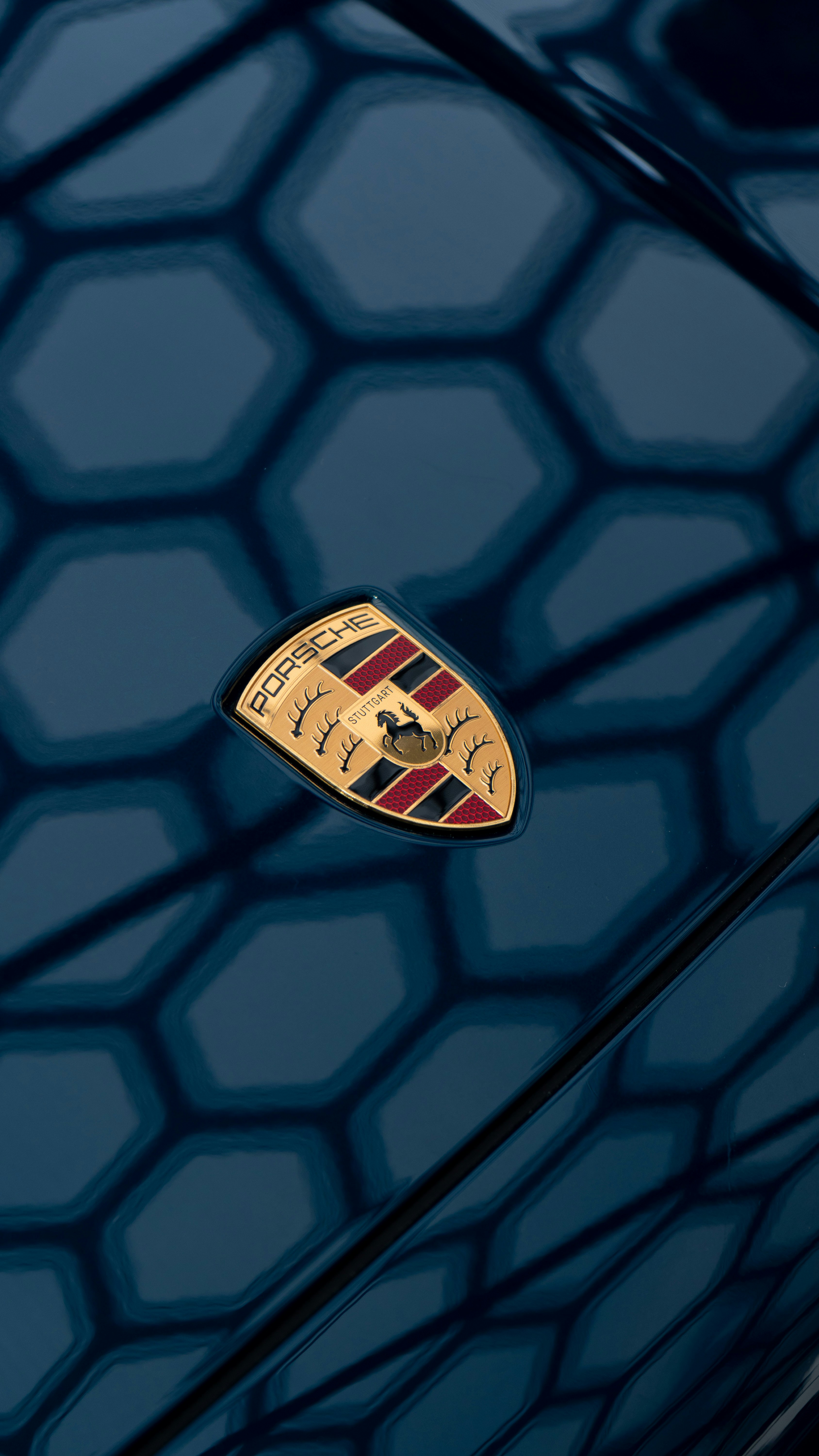 Emblem on blue tessellated hood: Porsche crest amid geometric reflections