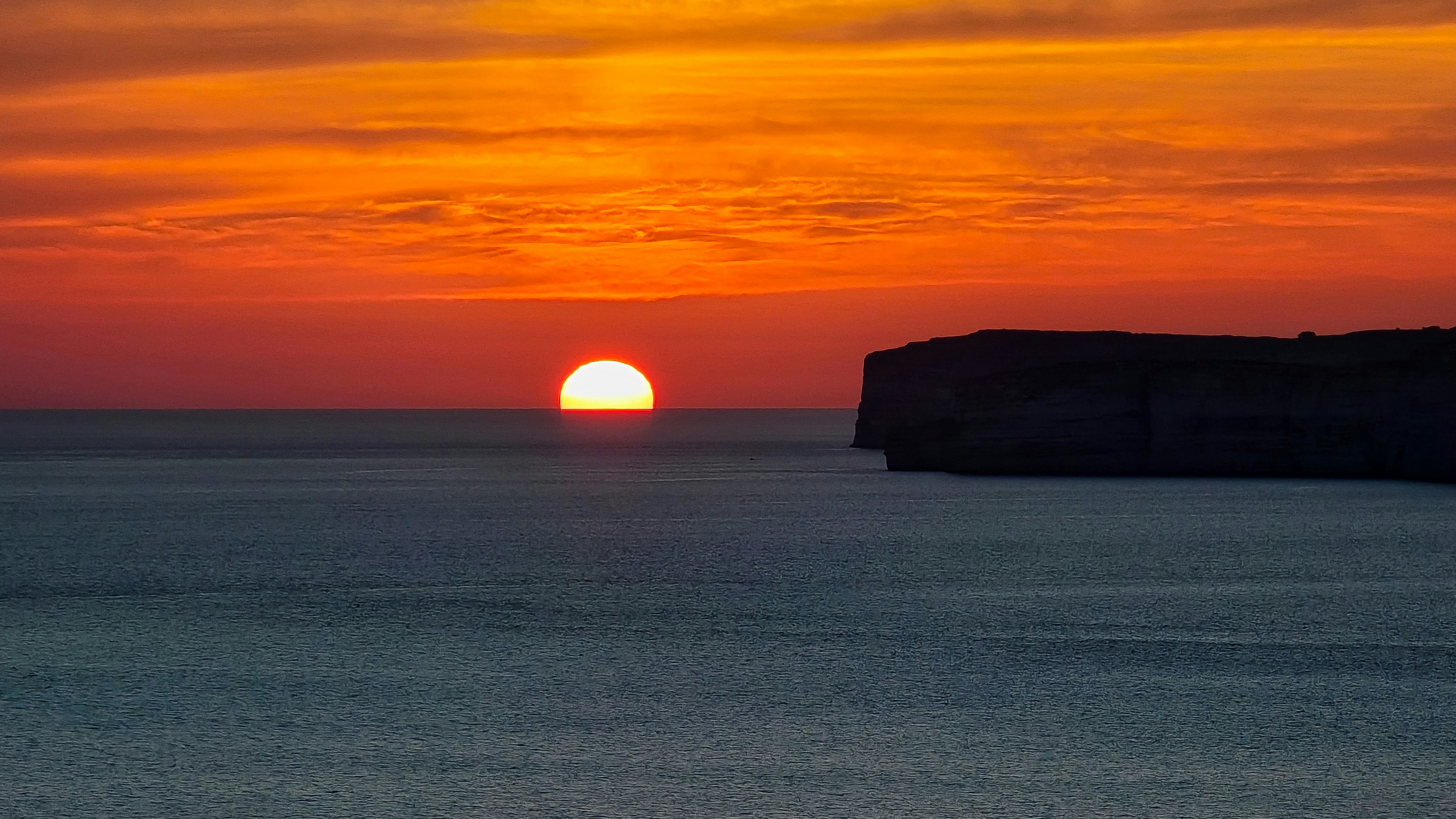 Setting Sun on a Quiet Sea: Horizon Bisected by Distant Cliff