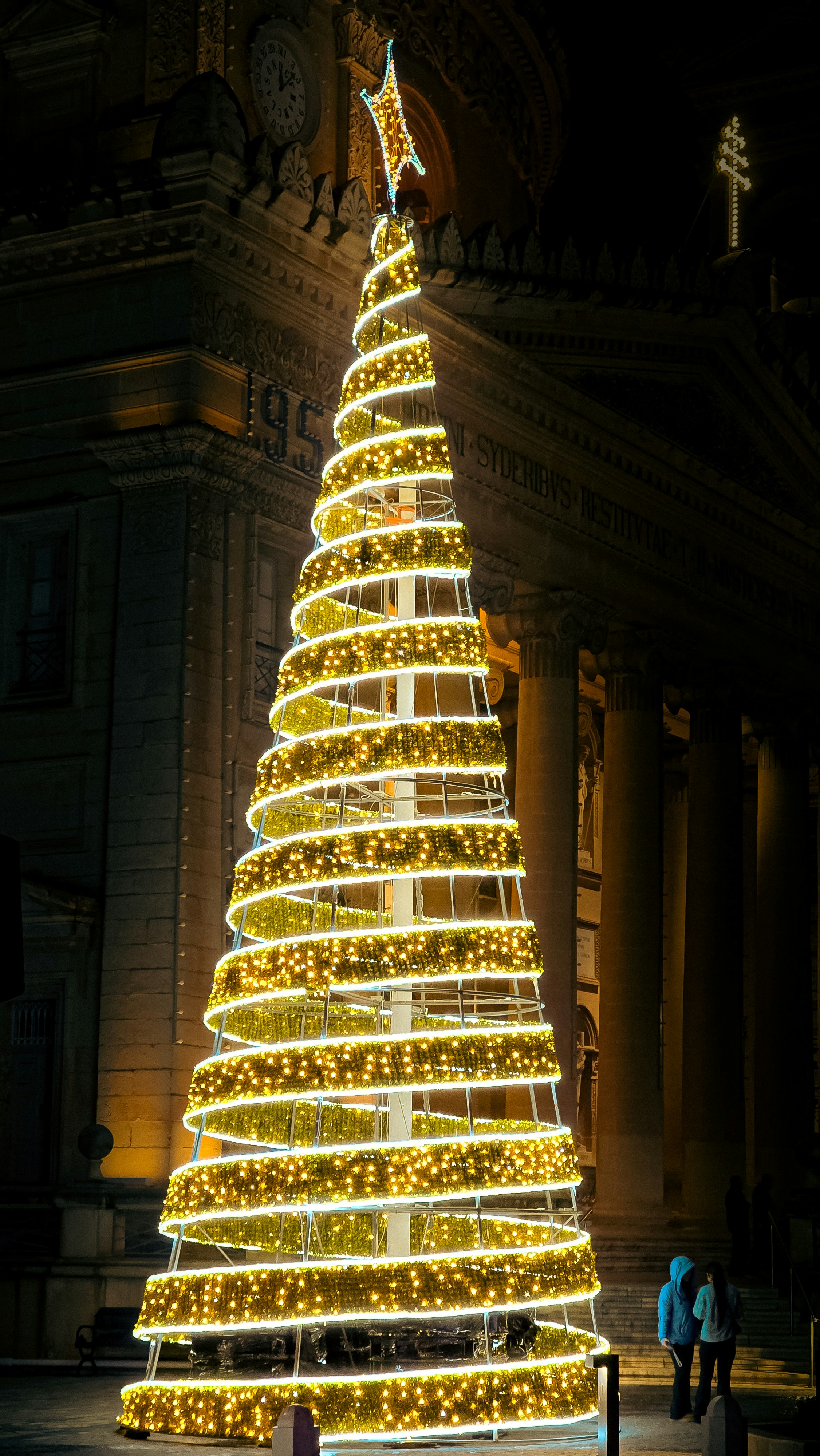 Glow Spiral: A Festive Tree Framed by Historic Facade at Night