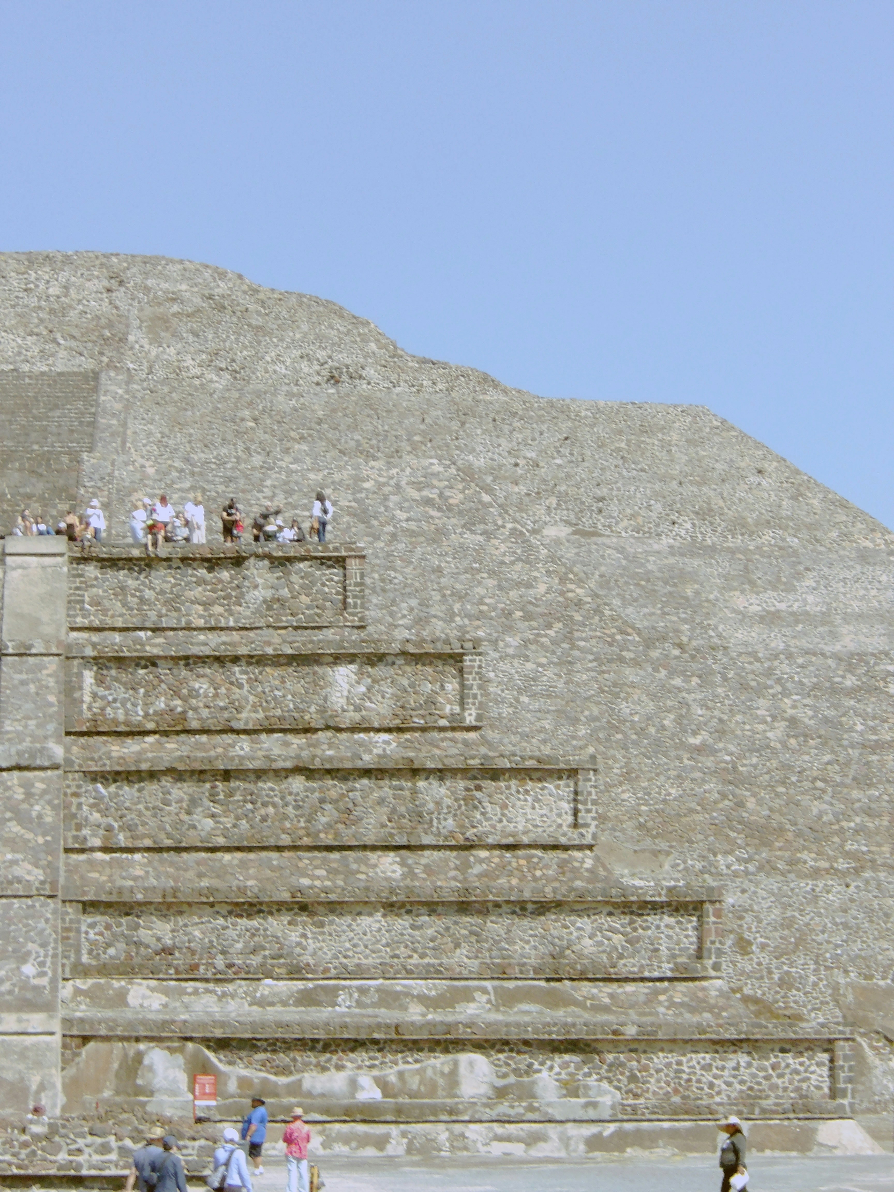 Tourists climb ancient stone steps under a clear blue sky.