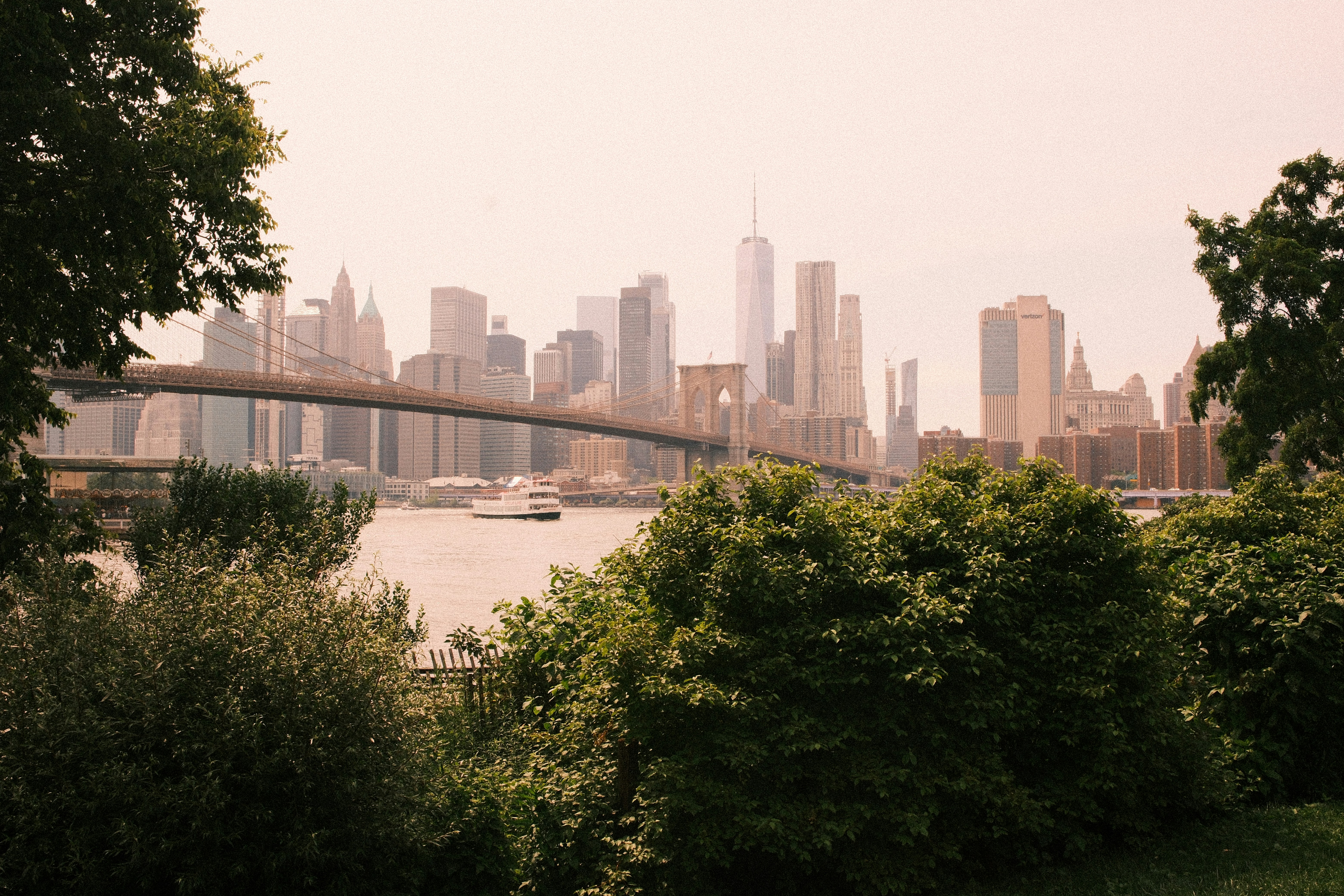 Cityscape Whim: Brooklyn Bridge and Skyline from a Lush Riverside Vantage