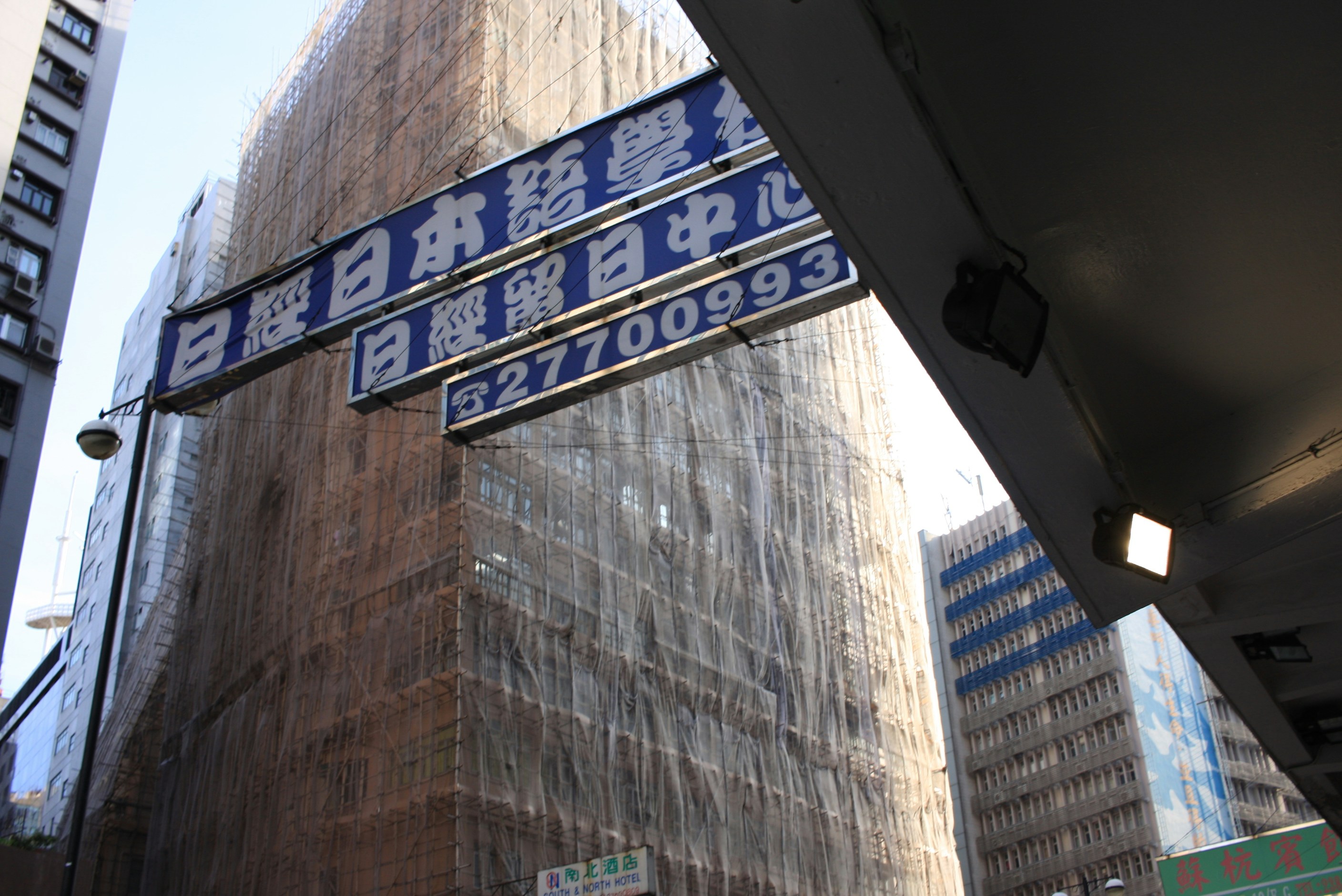 City scaffolding and skyward signage over a sunlit street canyon