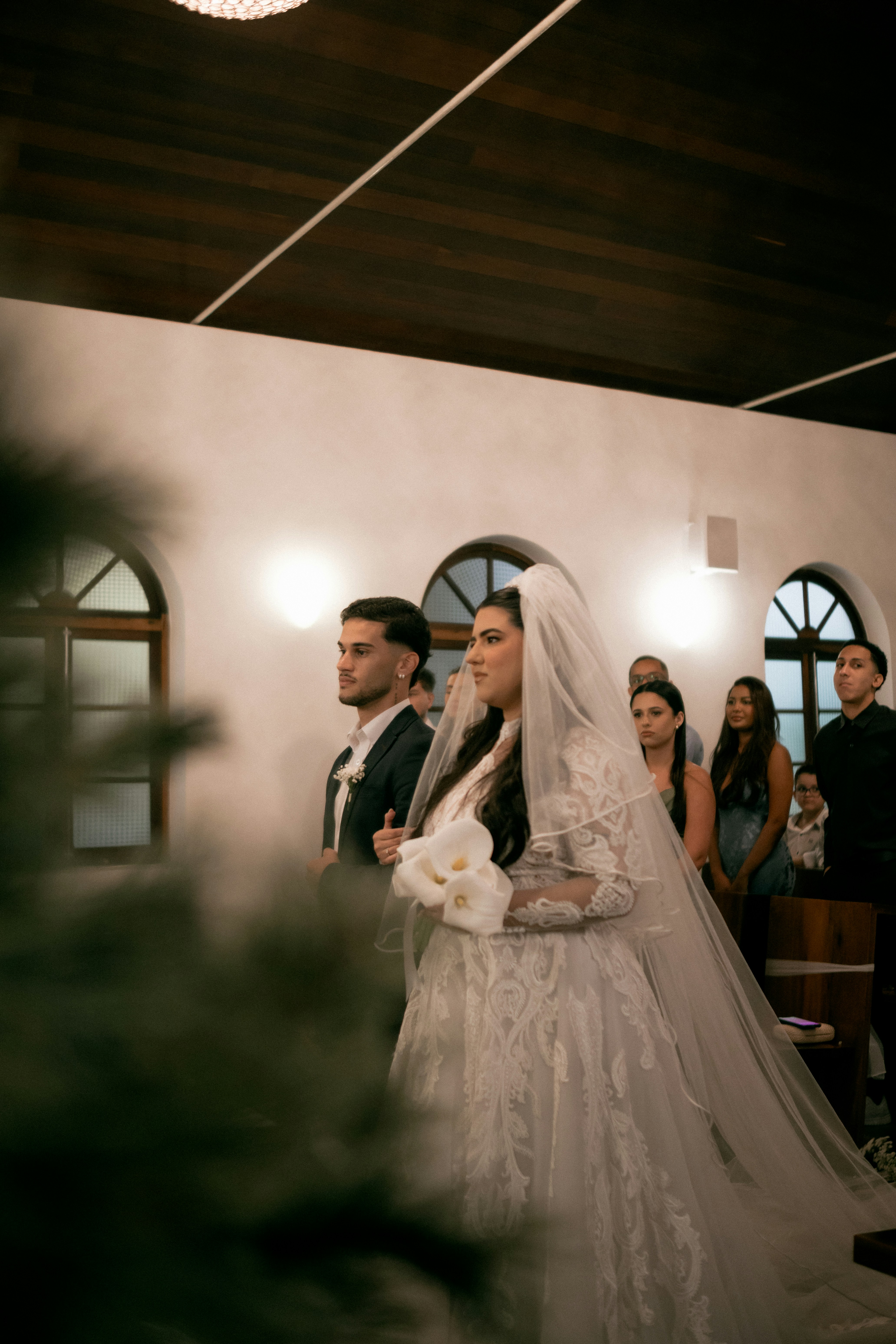Bride and groom lead the ceremony amid guests inside a warmly lit hall