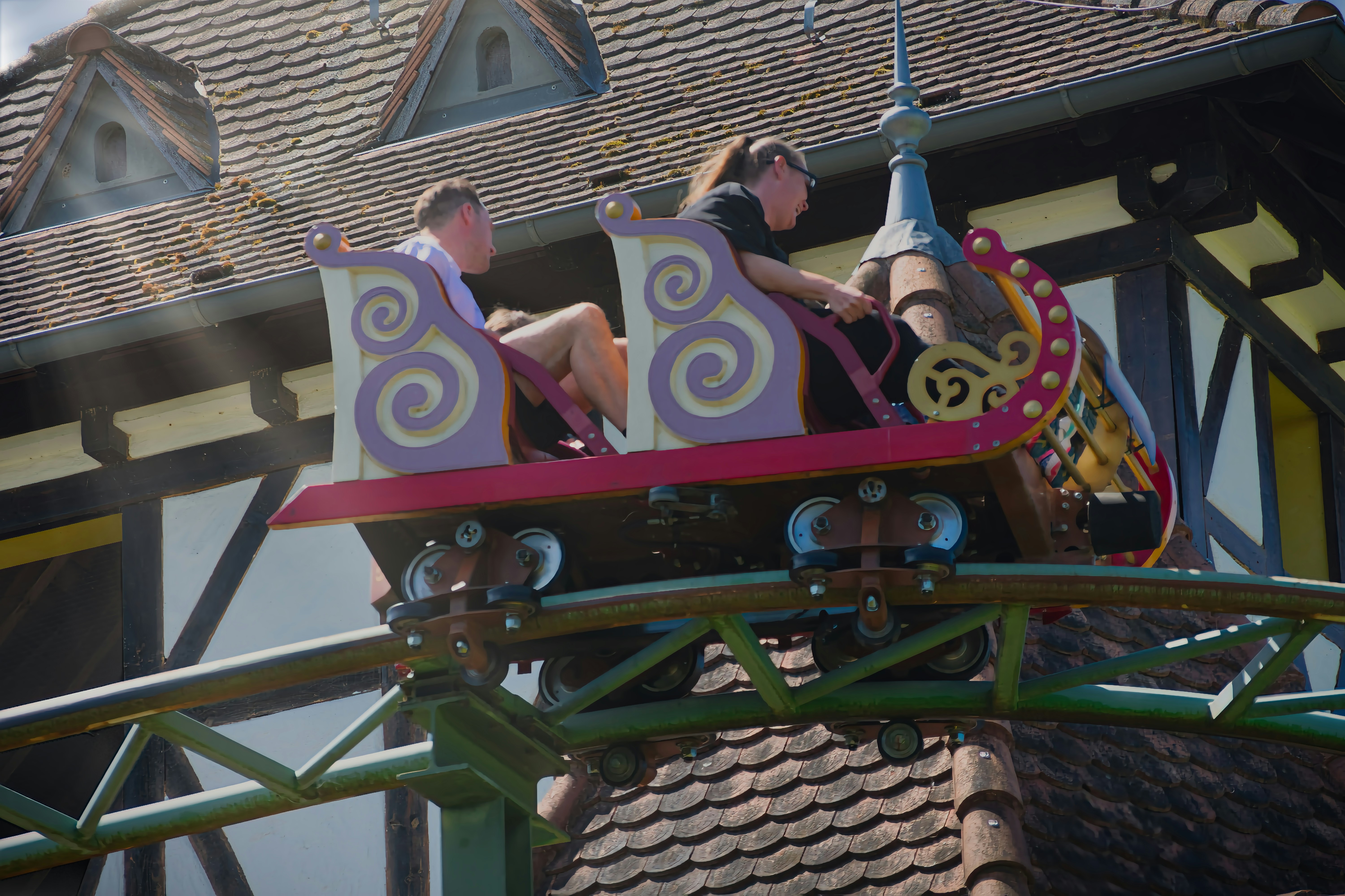 Suspended Thrill: Riders in a Colorful Car Climb Above the Rooflines