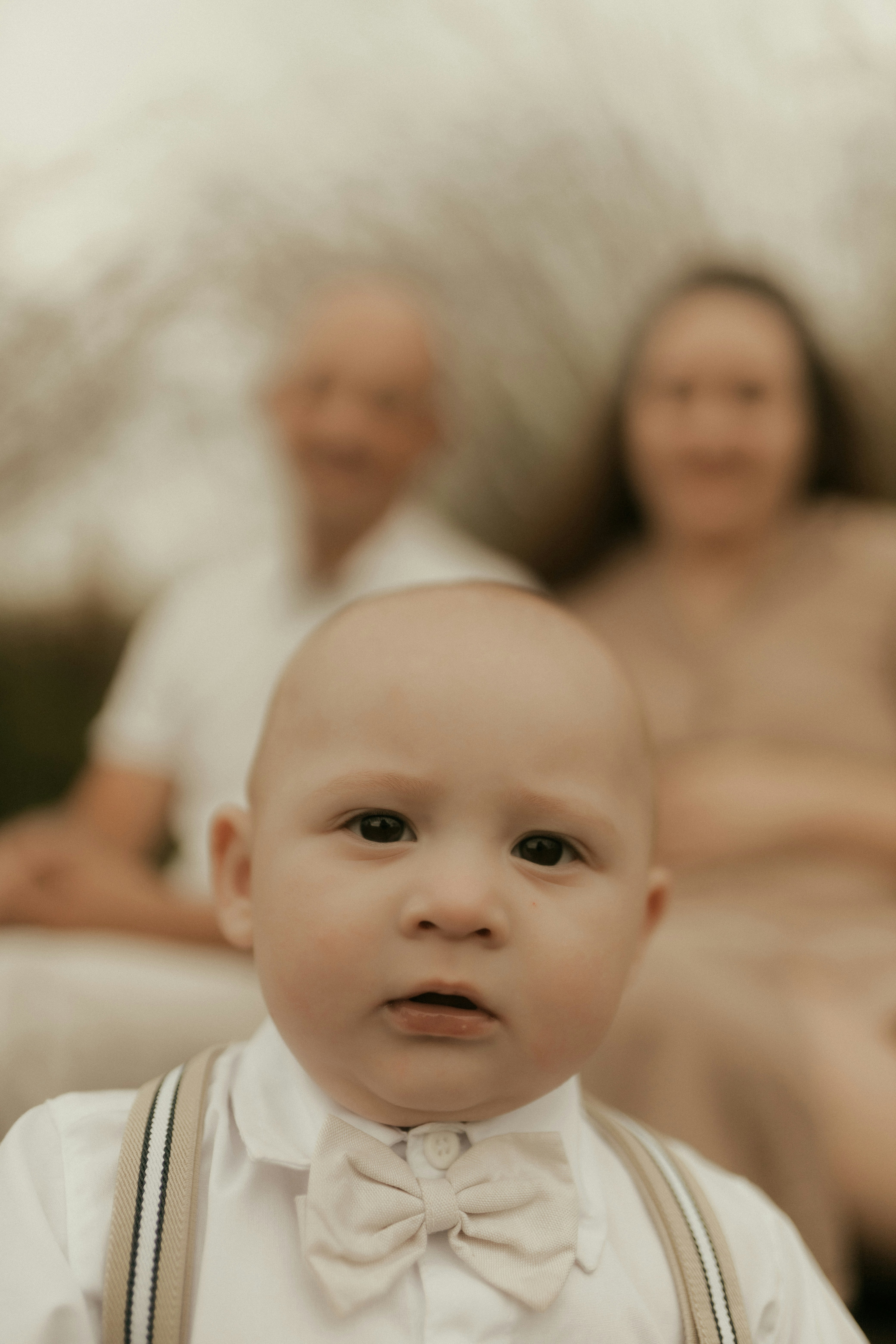 Close-Up of a Baby in a White Bow Tie with Soft-Focused Family in Background