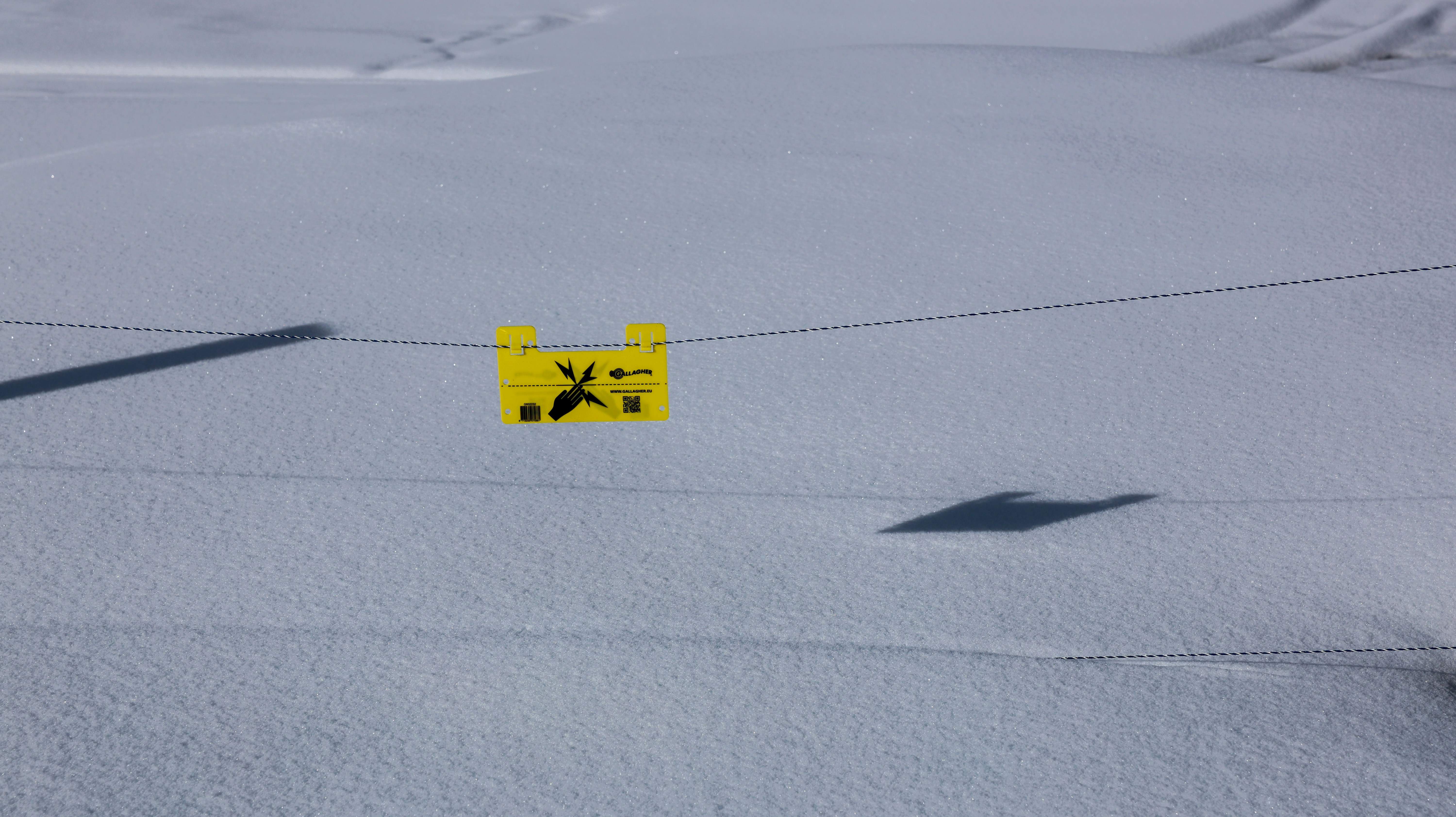 Yellow warning sign on snowy slope under minimal shadows
