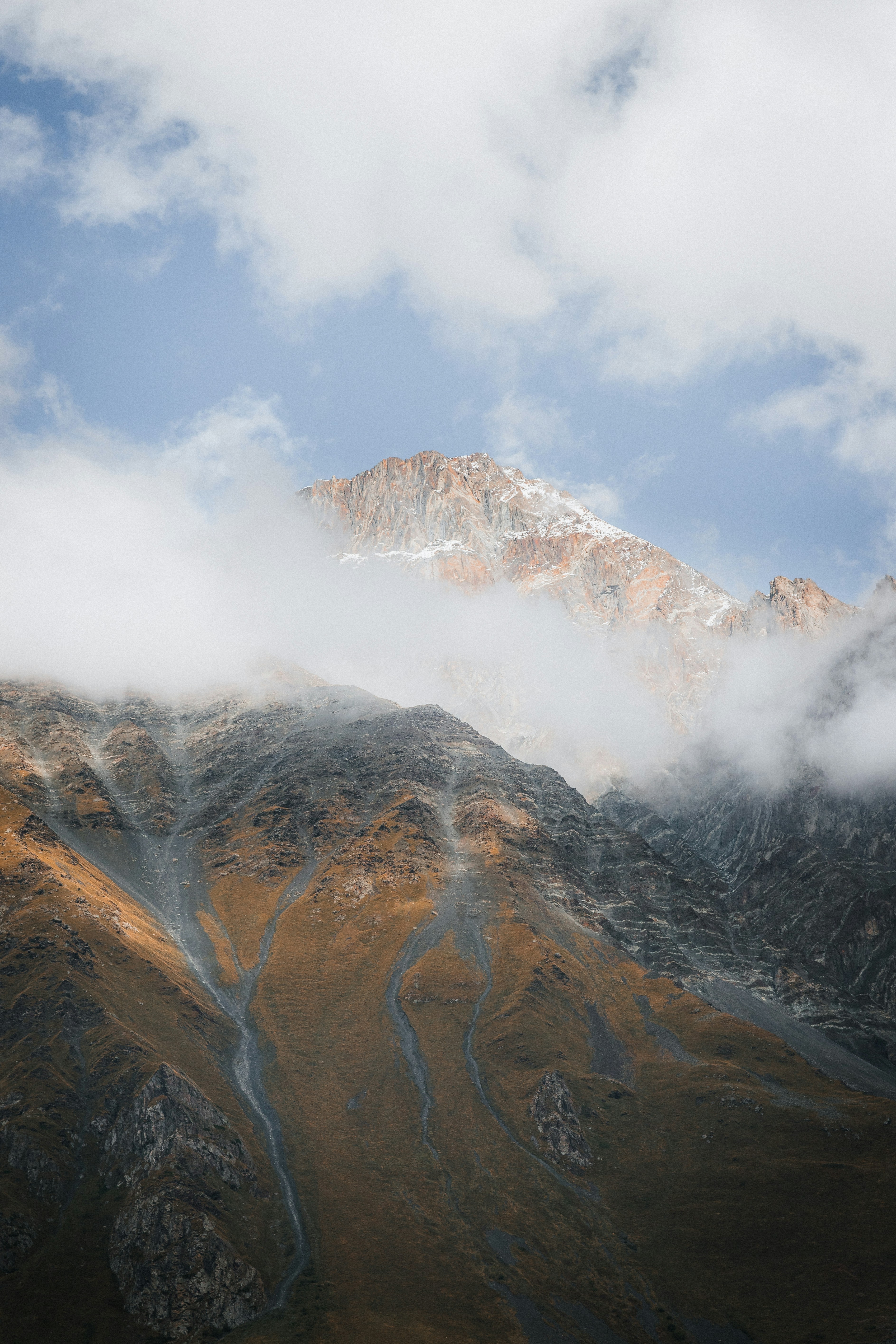 Snow-capped Peak Emerging Through Low Clouds Above Rugged Alpine Slopes
