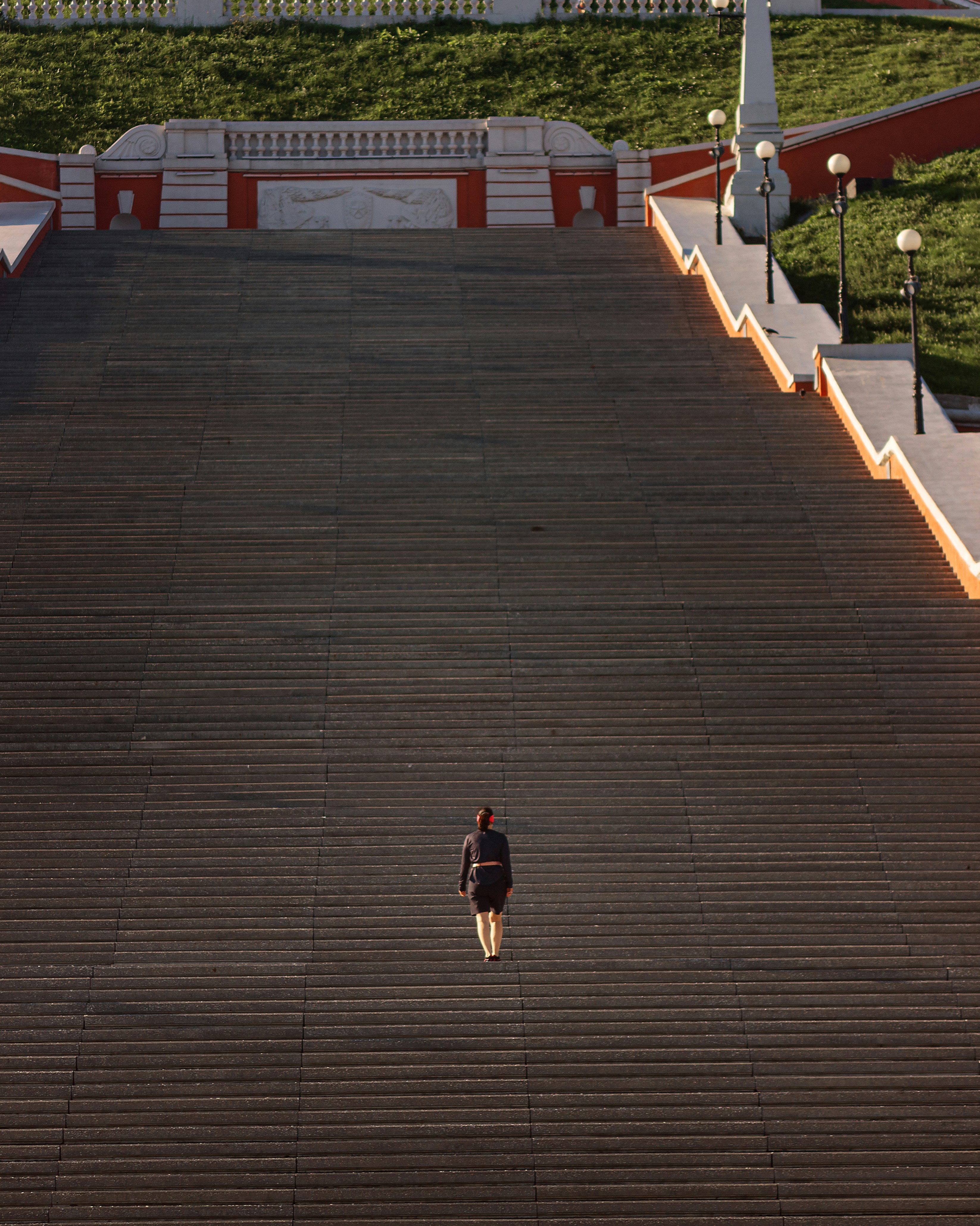 A lone figure ascends the grand staircase toward a sunlit terrace