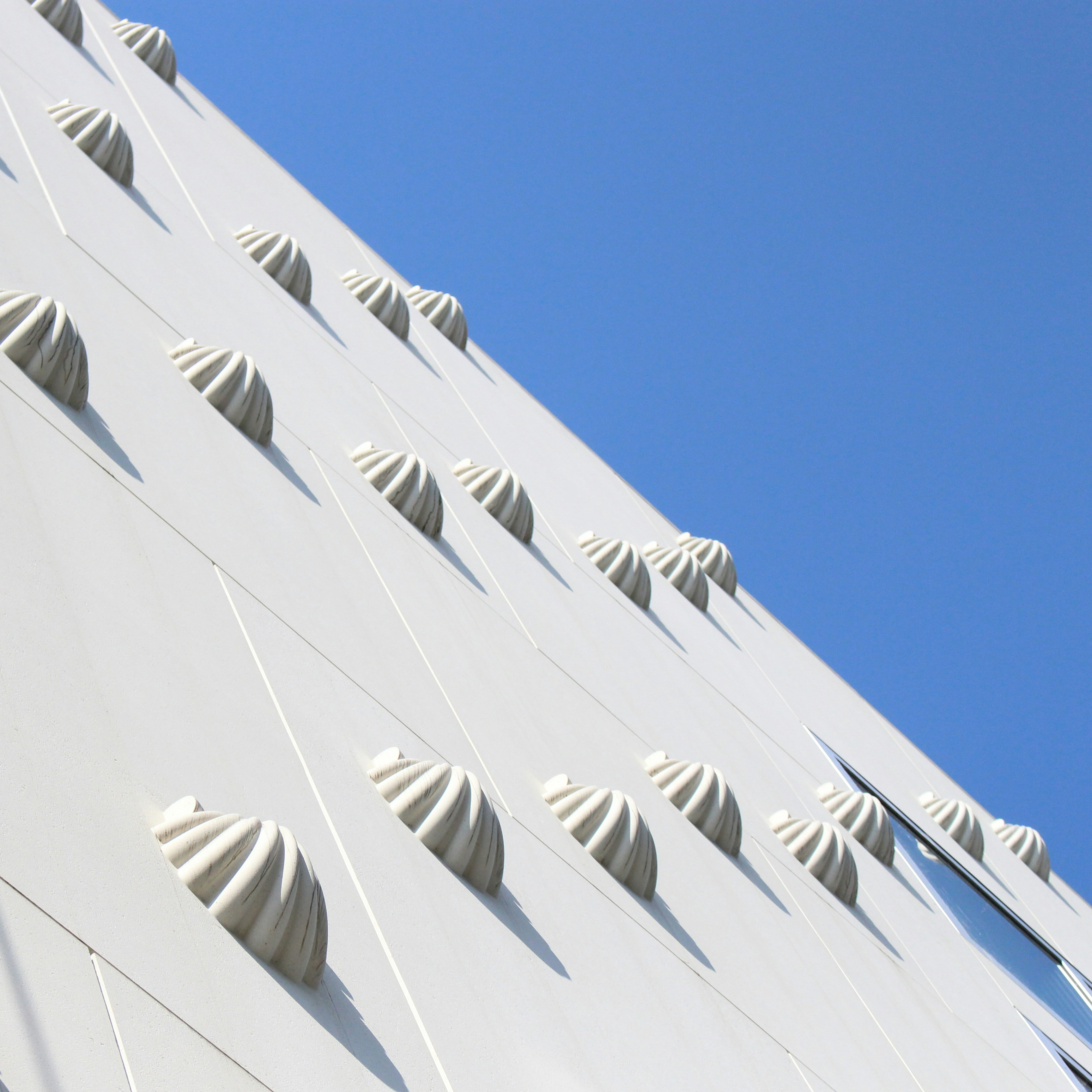 Bleached Facade Meets Blue Skies: Repeating Vent Nods on a tilted Surface