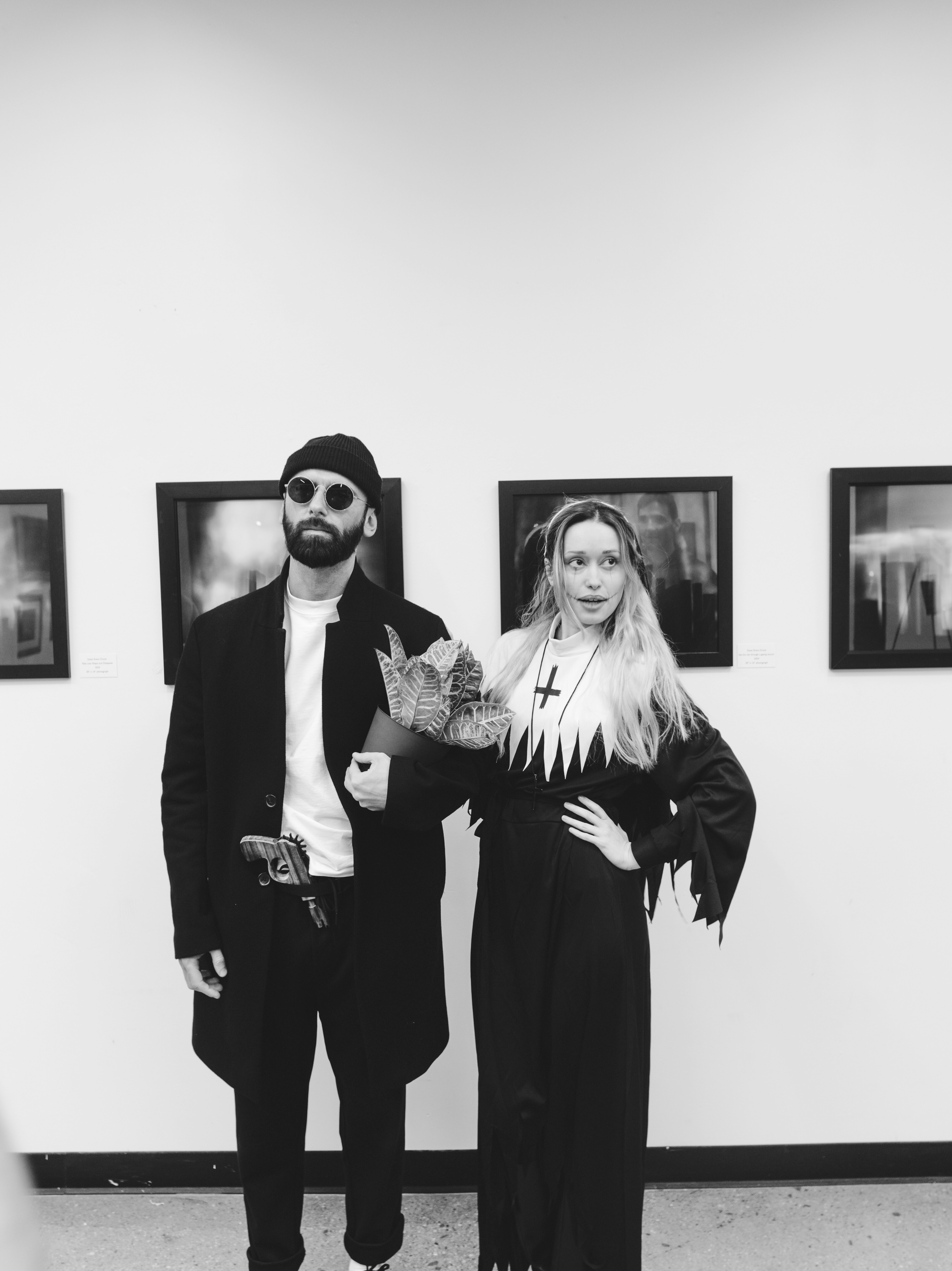 Two Costume-Clad Figures Stand Before Gallery Frames in a White-Walled Space