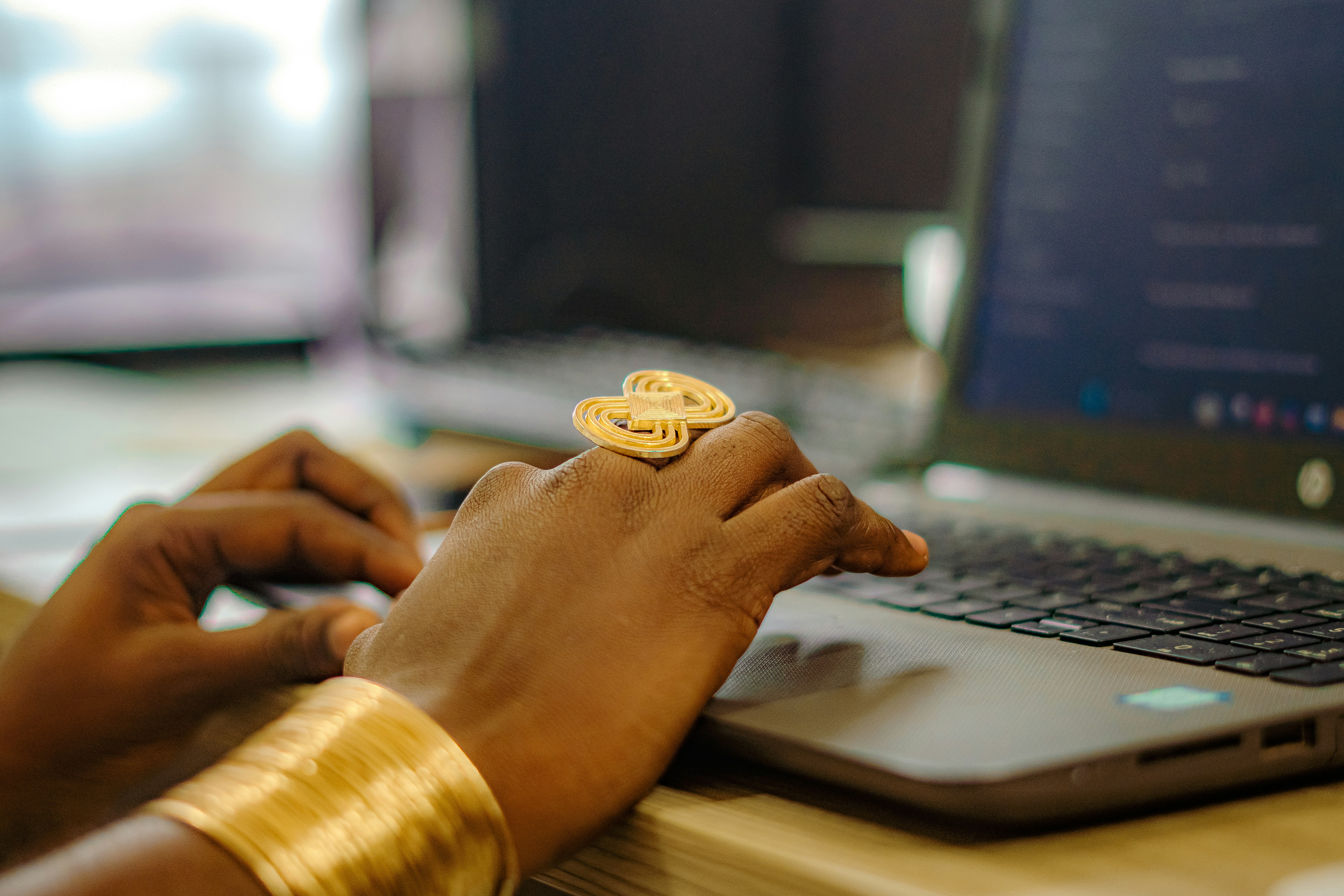Hands on a laptop: gold bangles and rings resting above the keyboard