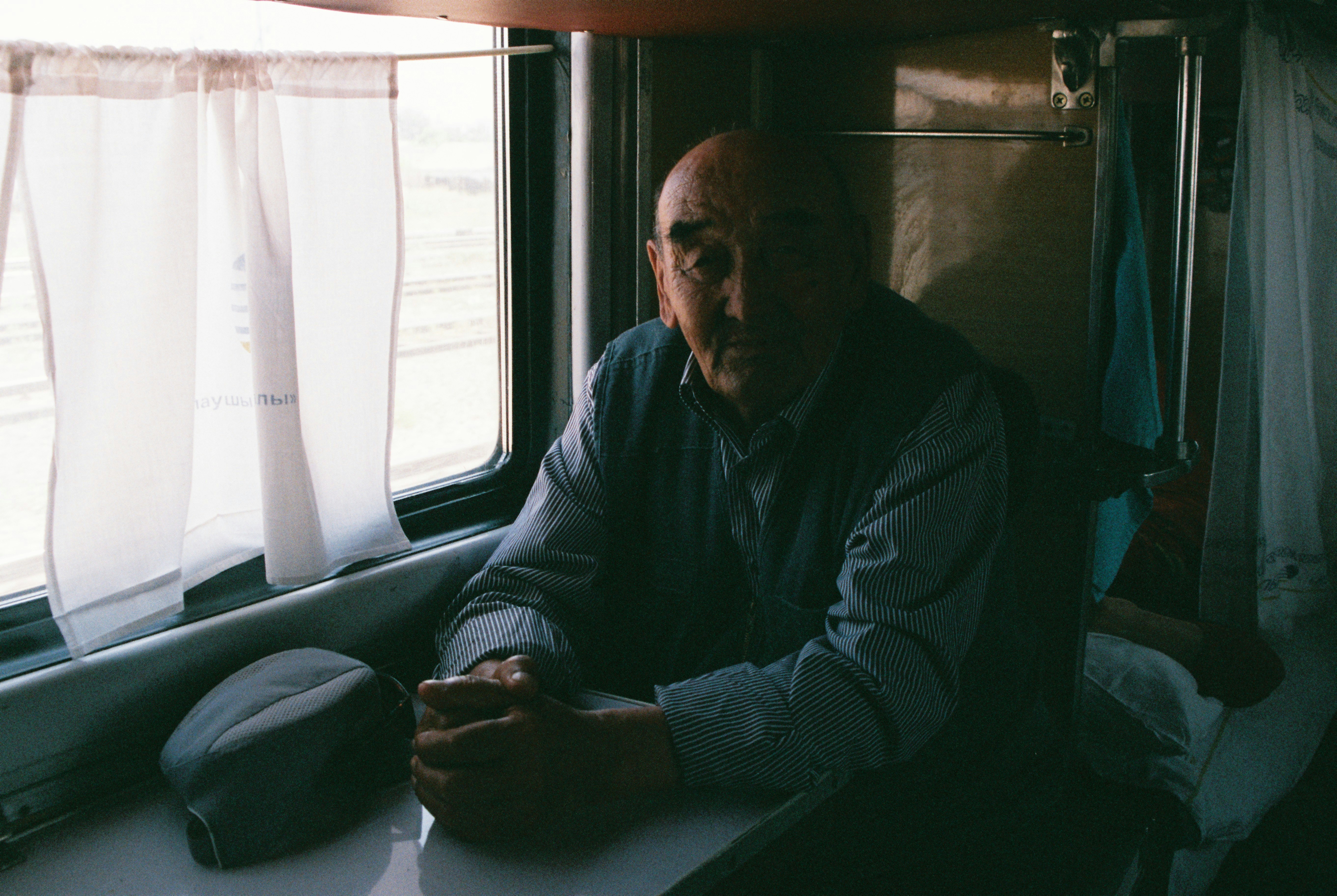 Eyebrowed Quiet: A Sleeper Train Passenger in Soft Window Light
