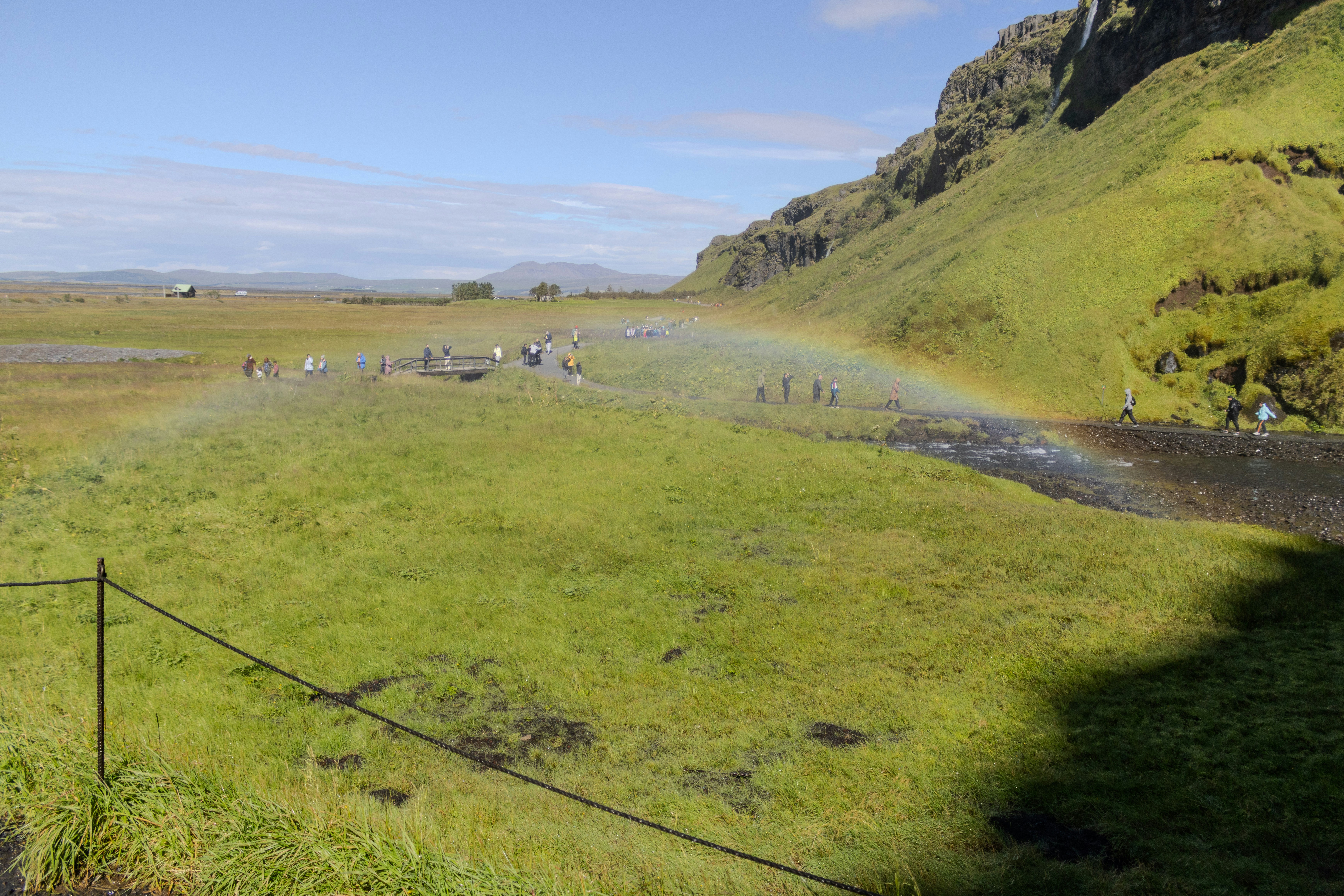 Steam over the grassy inlet: tourists by a shallow river with a cliffed hillside