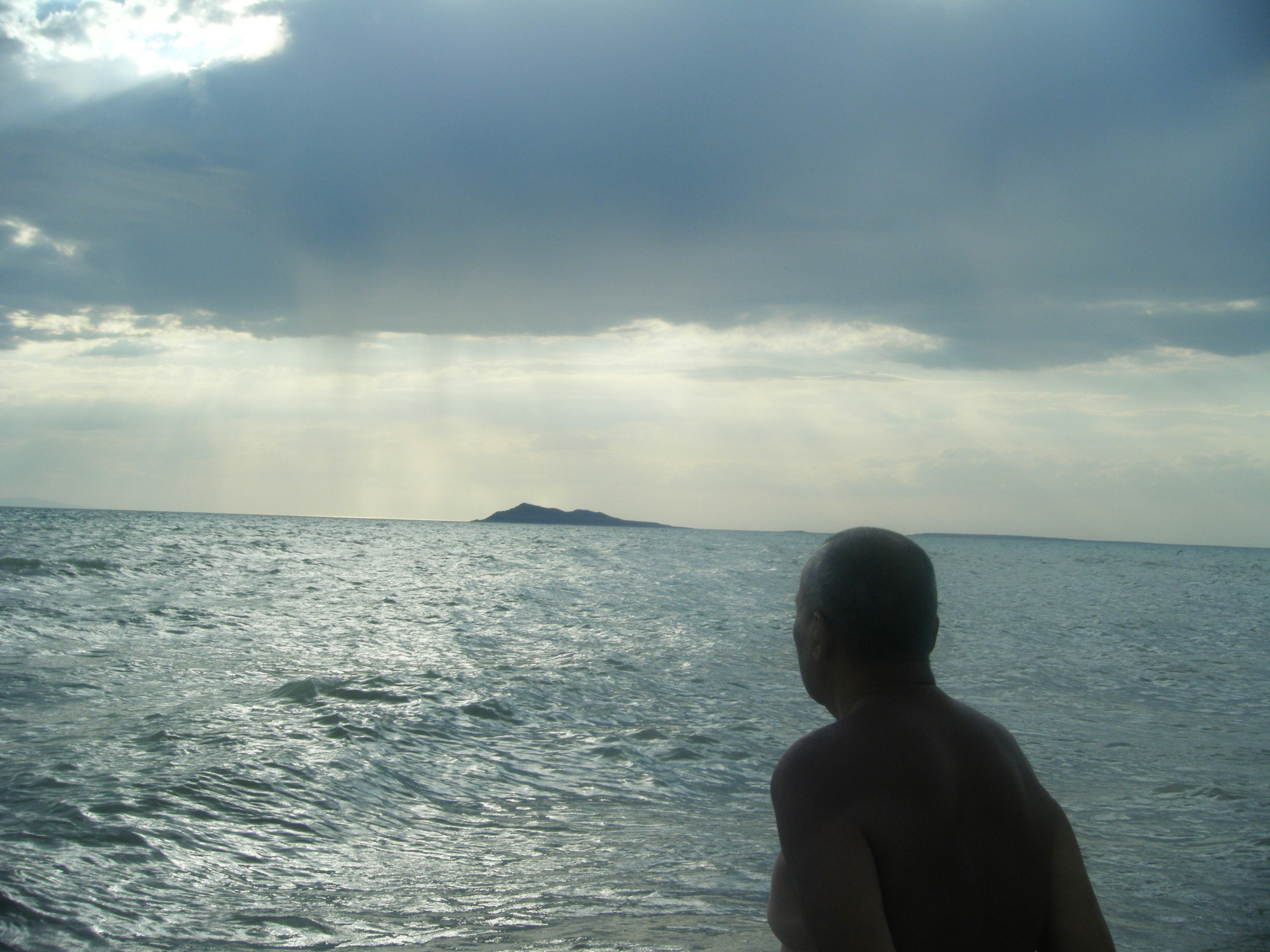 Man looking at island from beach at sunset