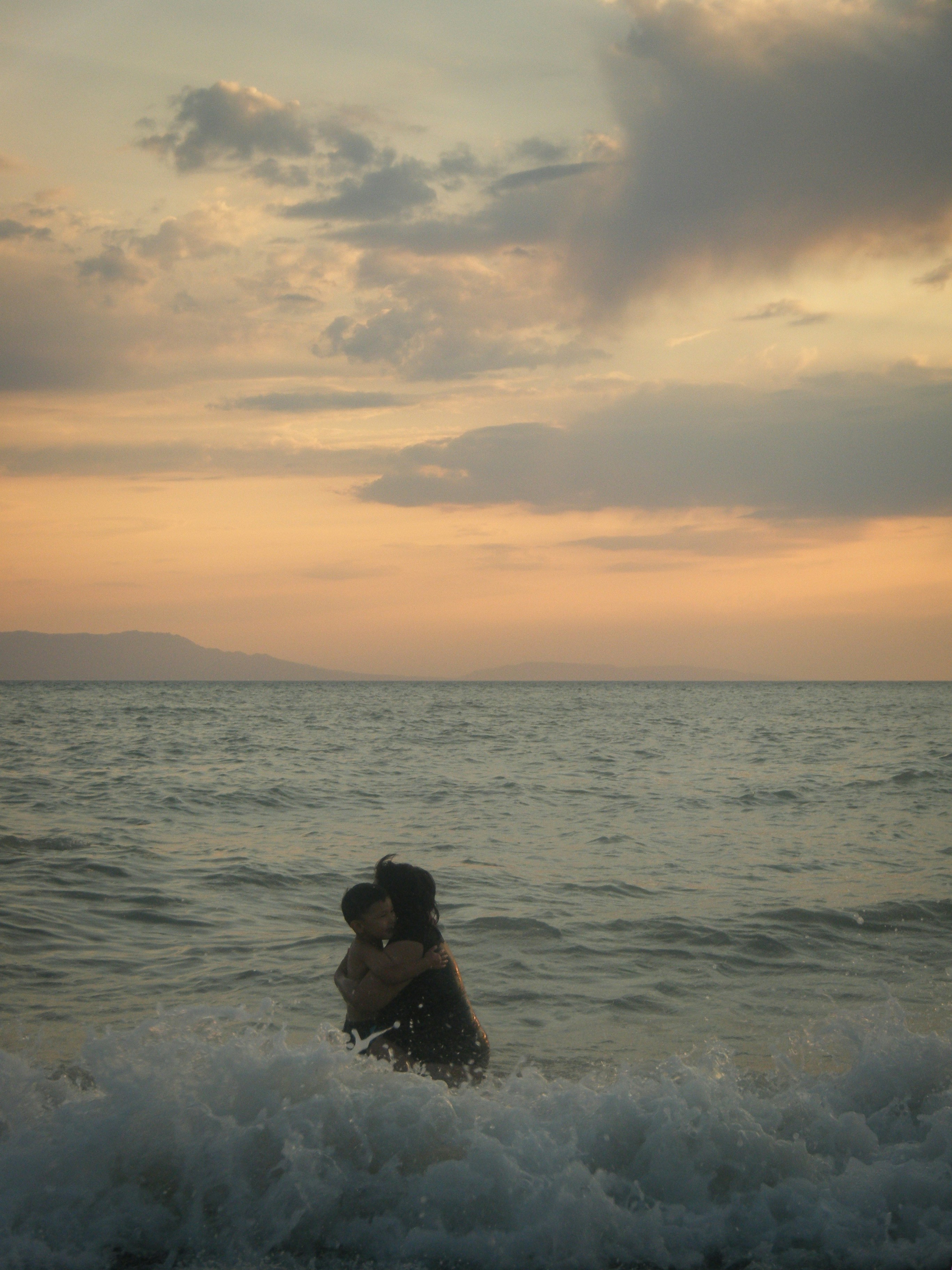 Couple embracing in ocean waves at sunset