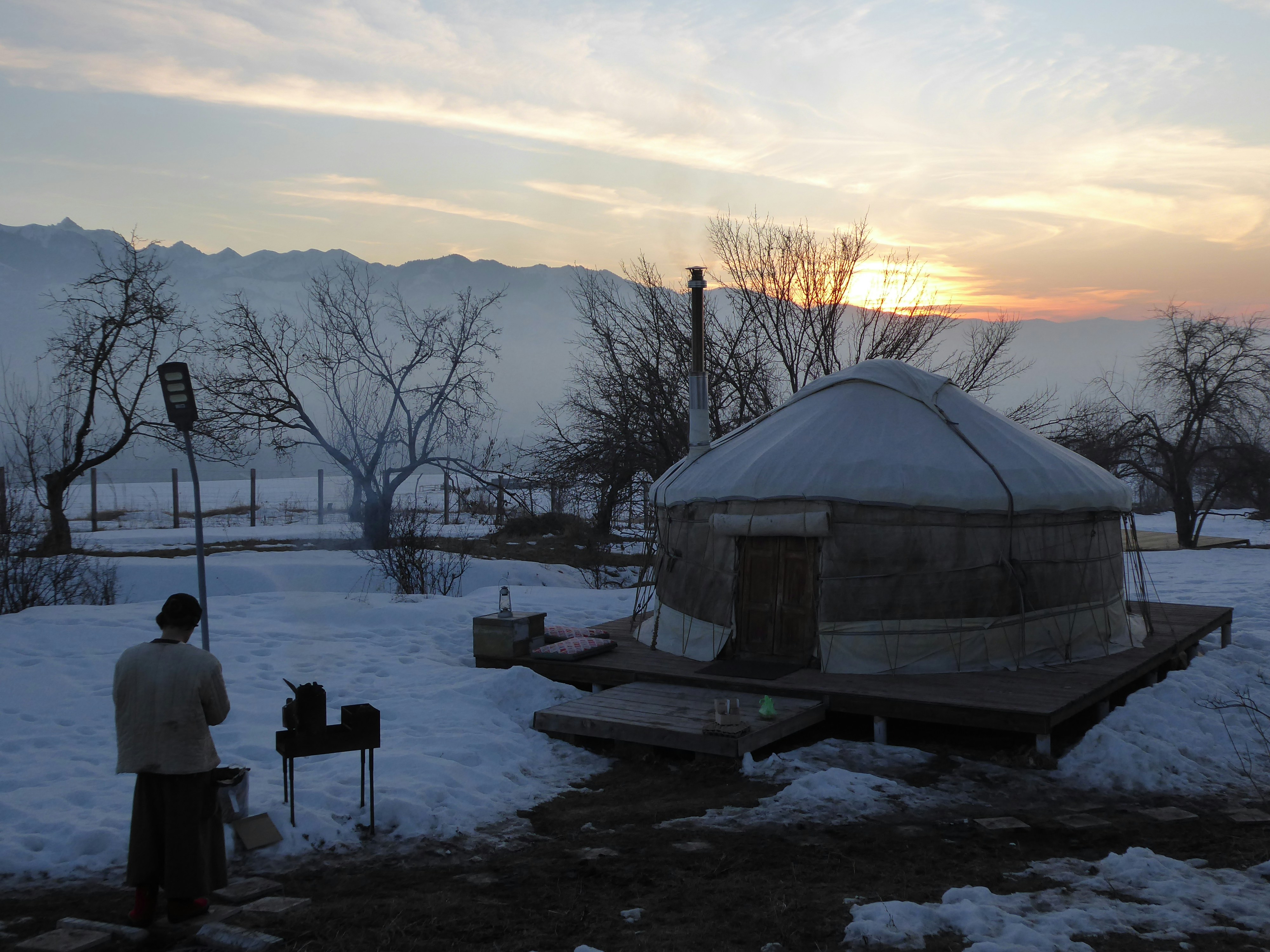 Person standing by a yurt in snowy landscape at sunset