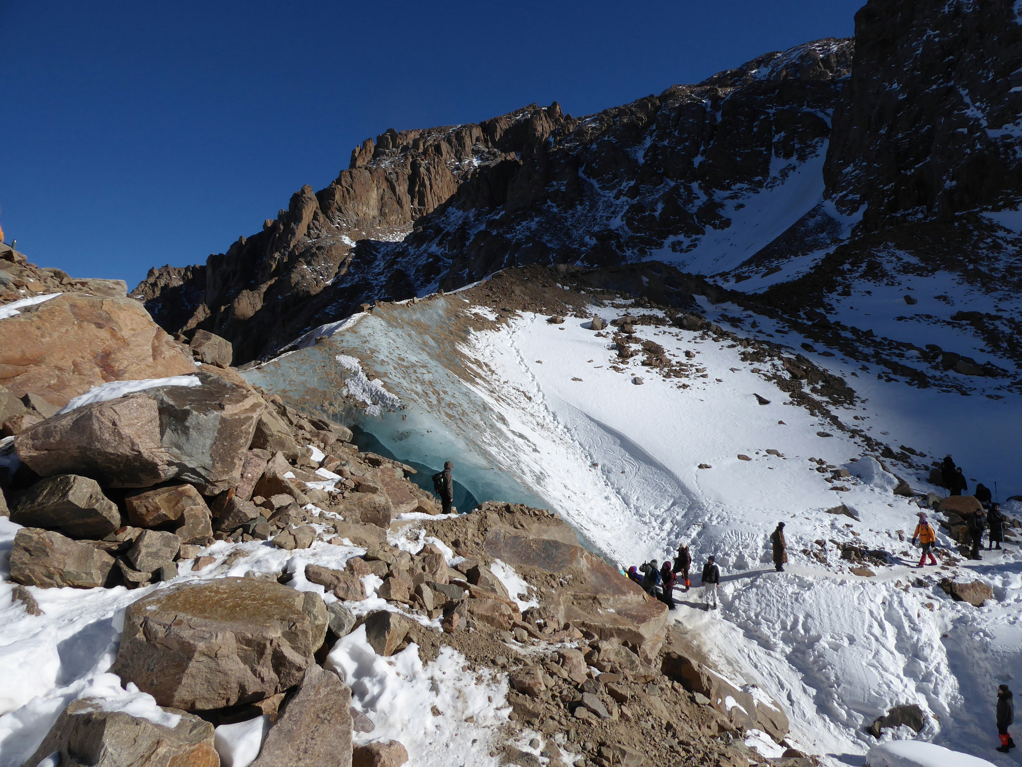 People gathered near a glacial ice formation in snowy mountains.