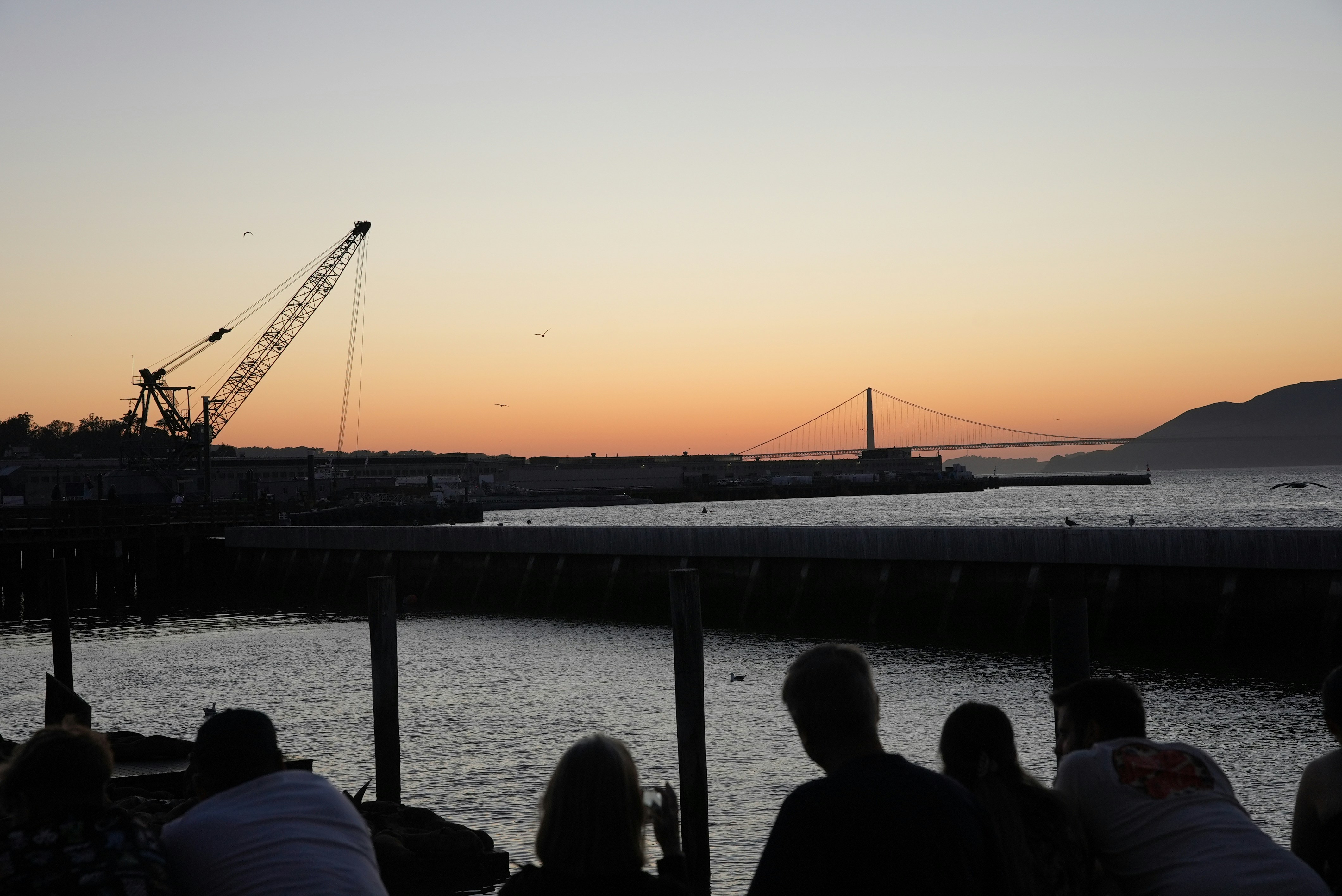 Sunset at the Pier: silhouettes and distant crane under a pale horizon