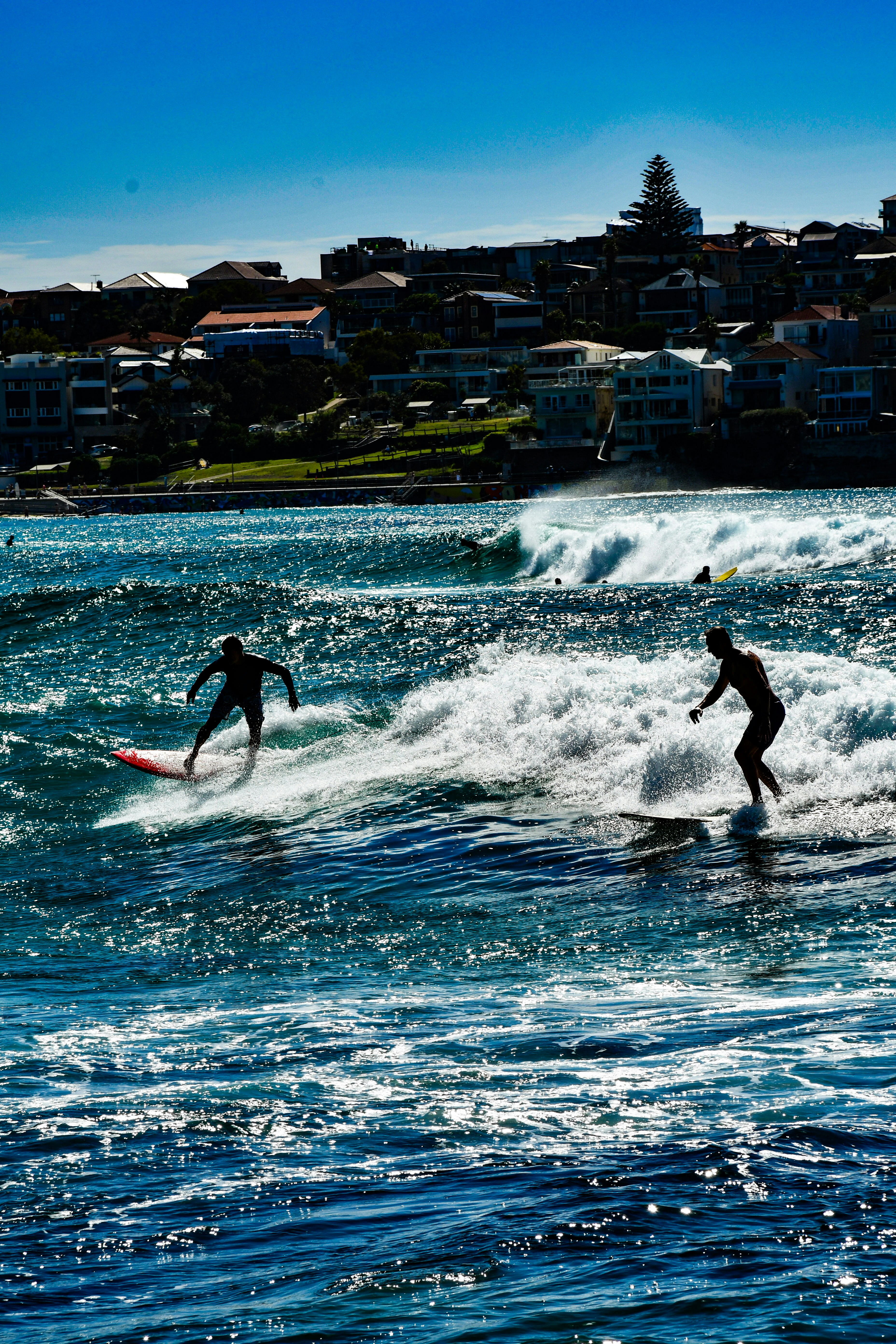 Two surfers carve turquoise swells under a coastal neighborhood