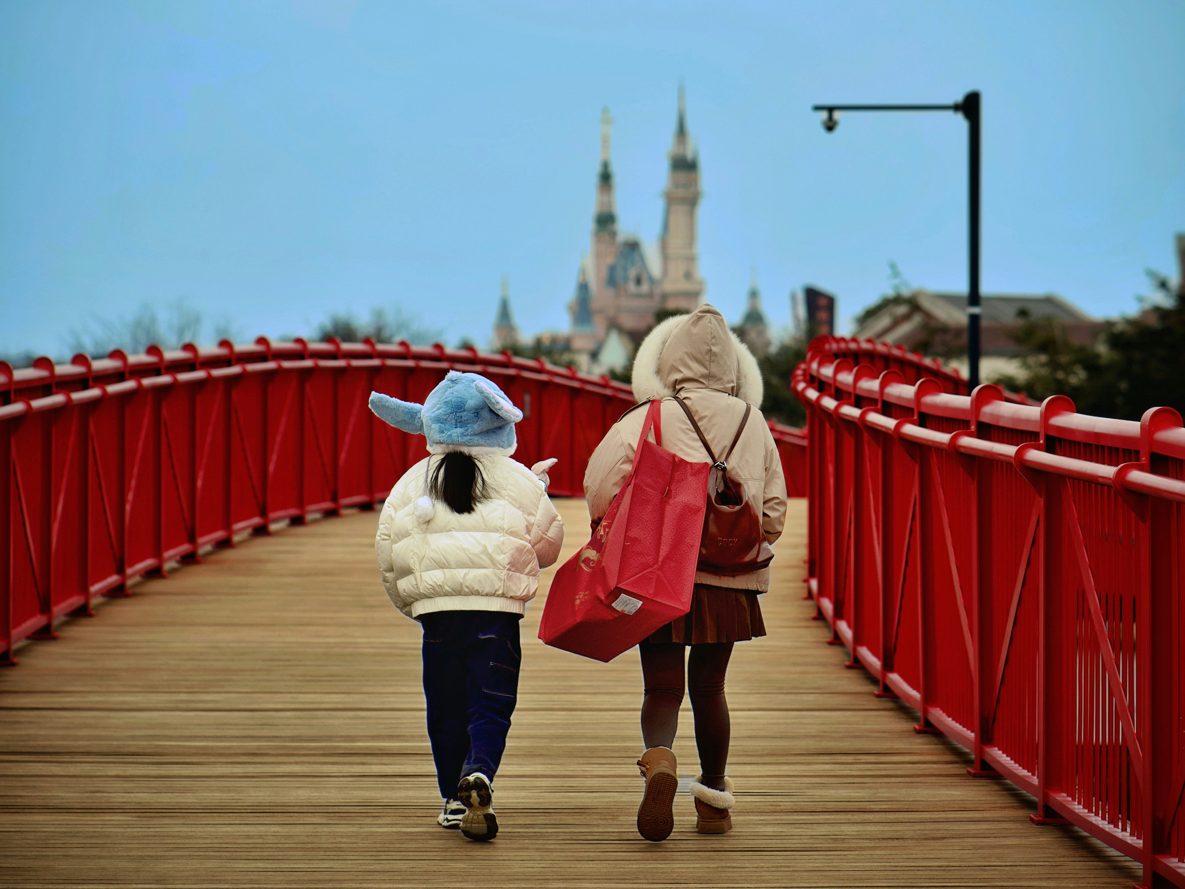 Two travelers on a red-rail bridge toward a distant castle