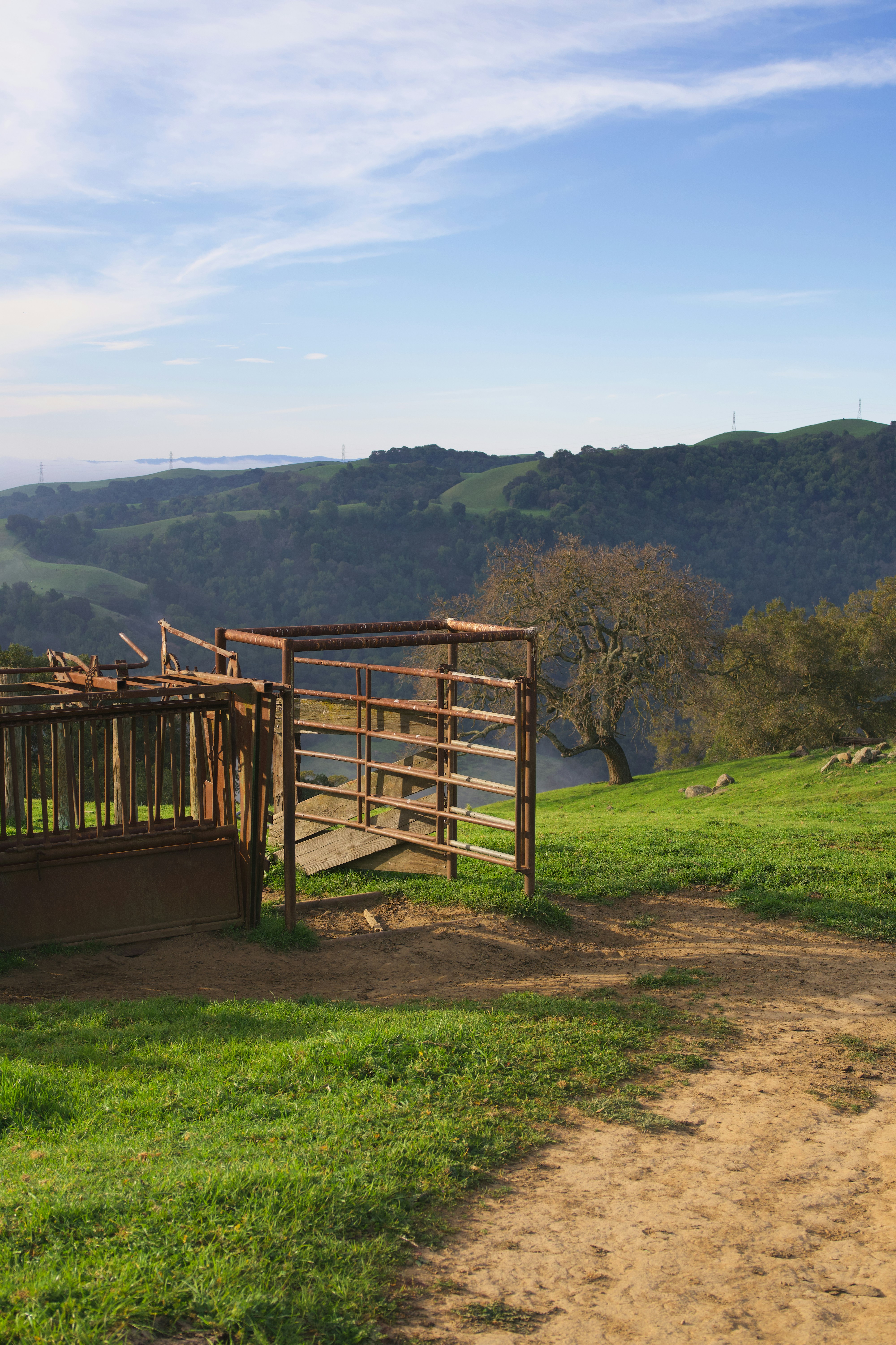 Rusted gate opened toward a rolling valley under a bright sky