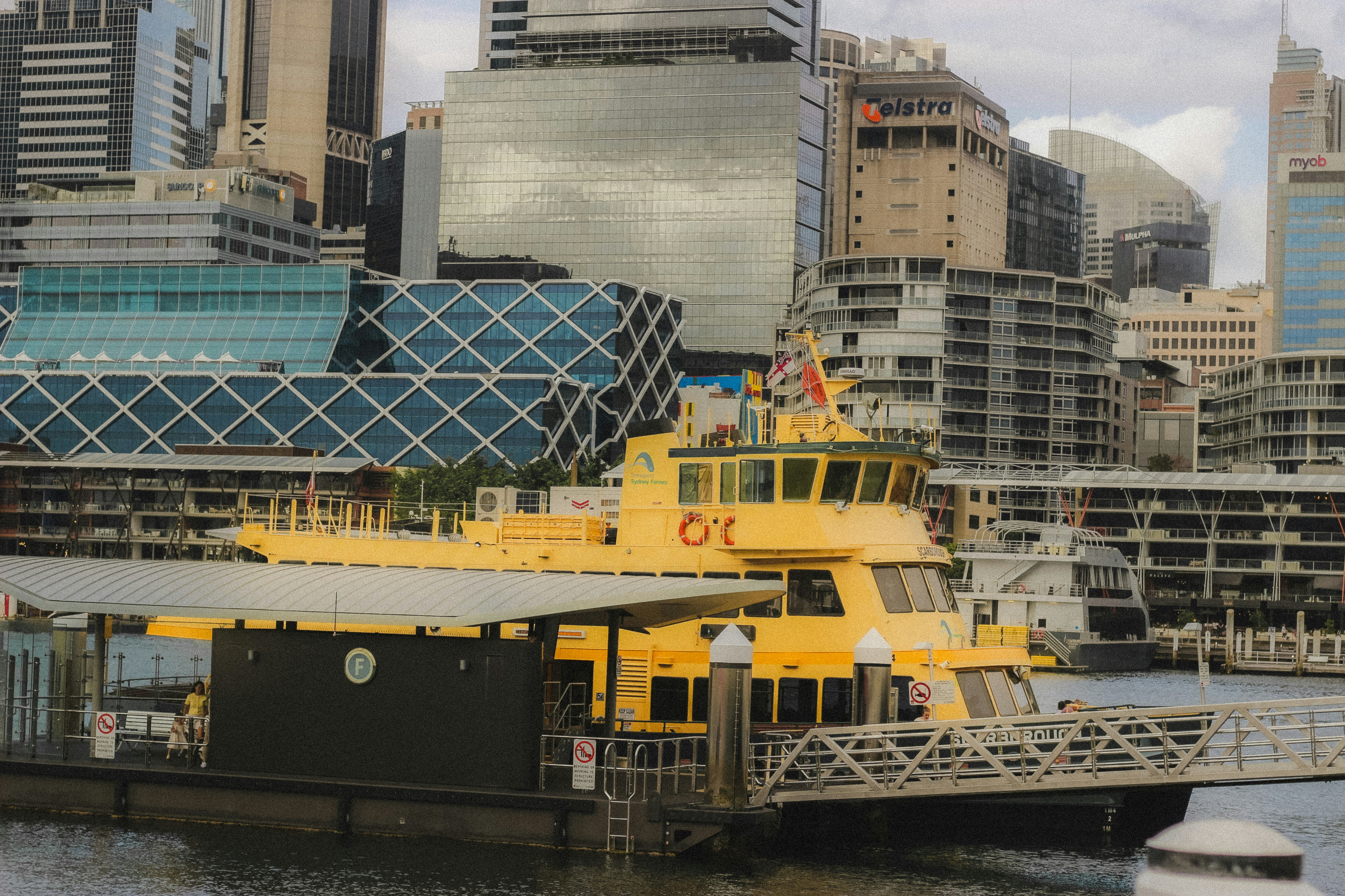 Yellow Multi-Deck Ferry Anchored Against a Modern City Skyline