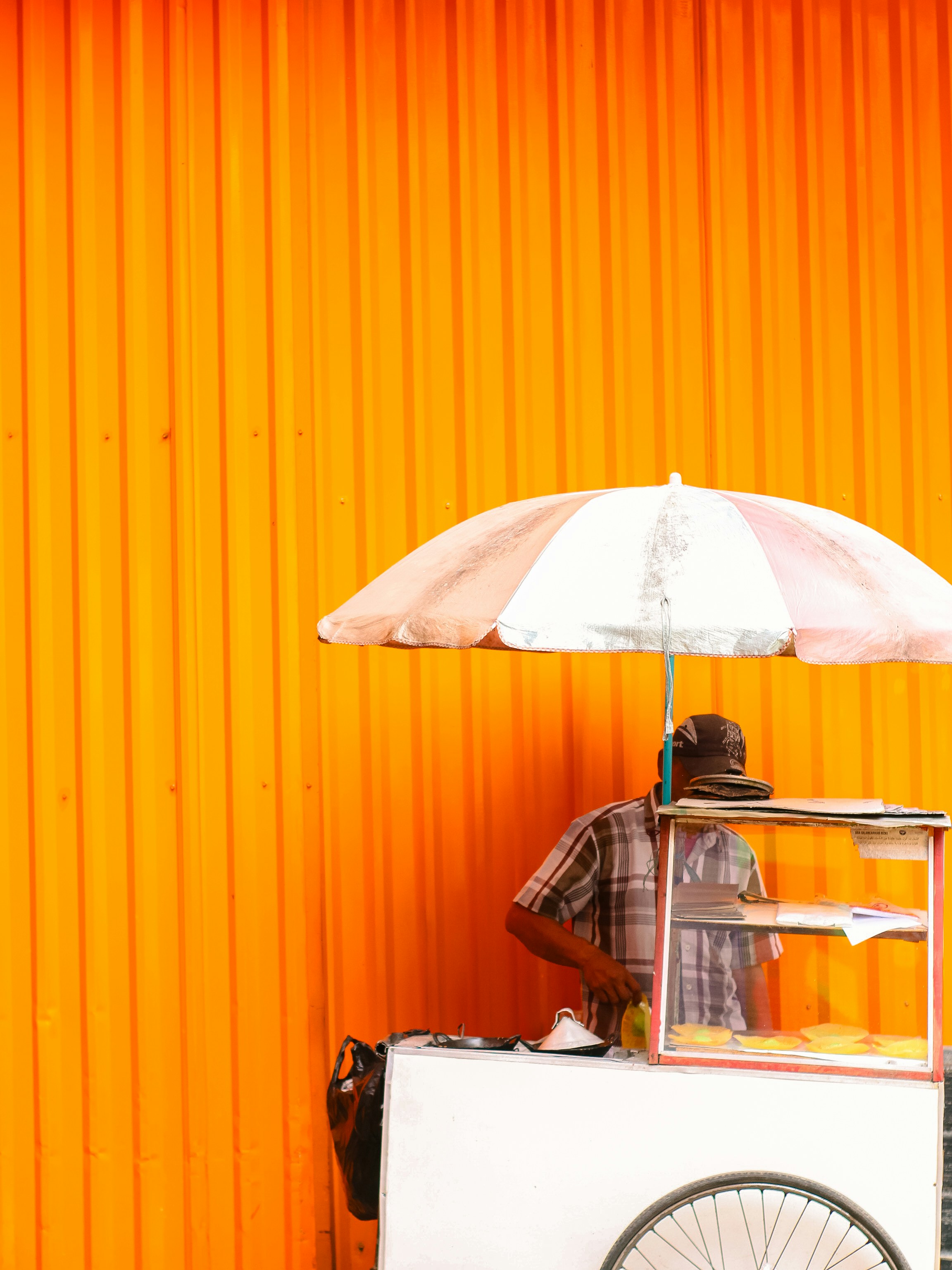 Street Cart Under a Sunlit Umbrella Against a Bold Orange Wall