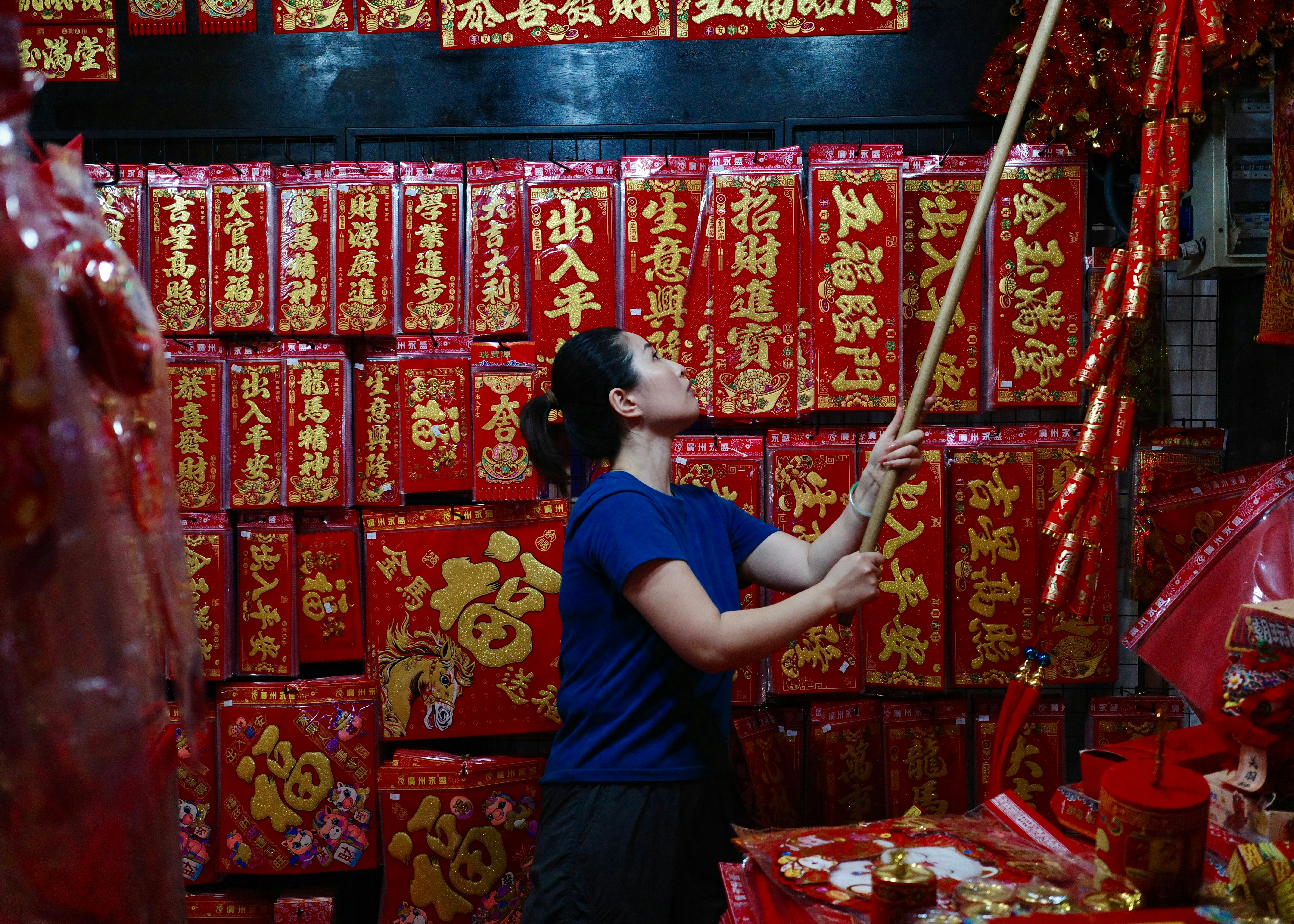 Crimson Offerings: A shopkeeper in a sea of red scrolls and lanterns