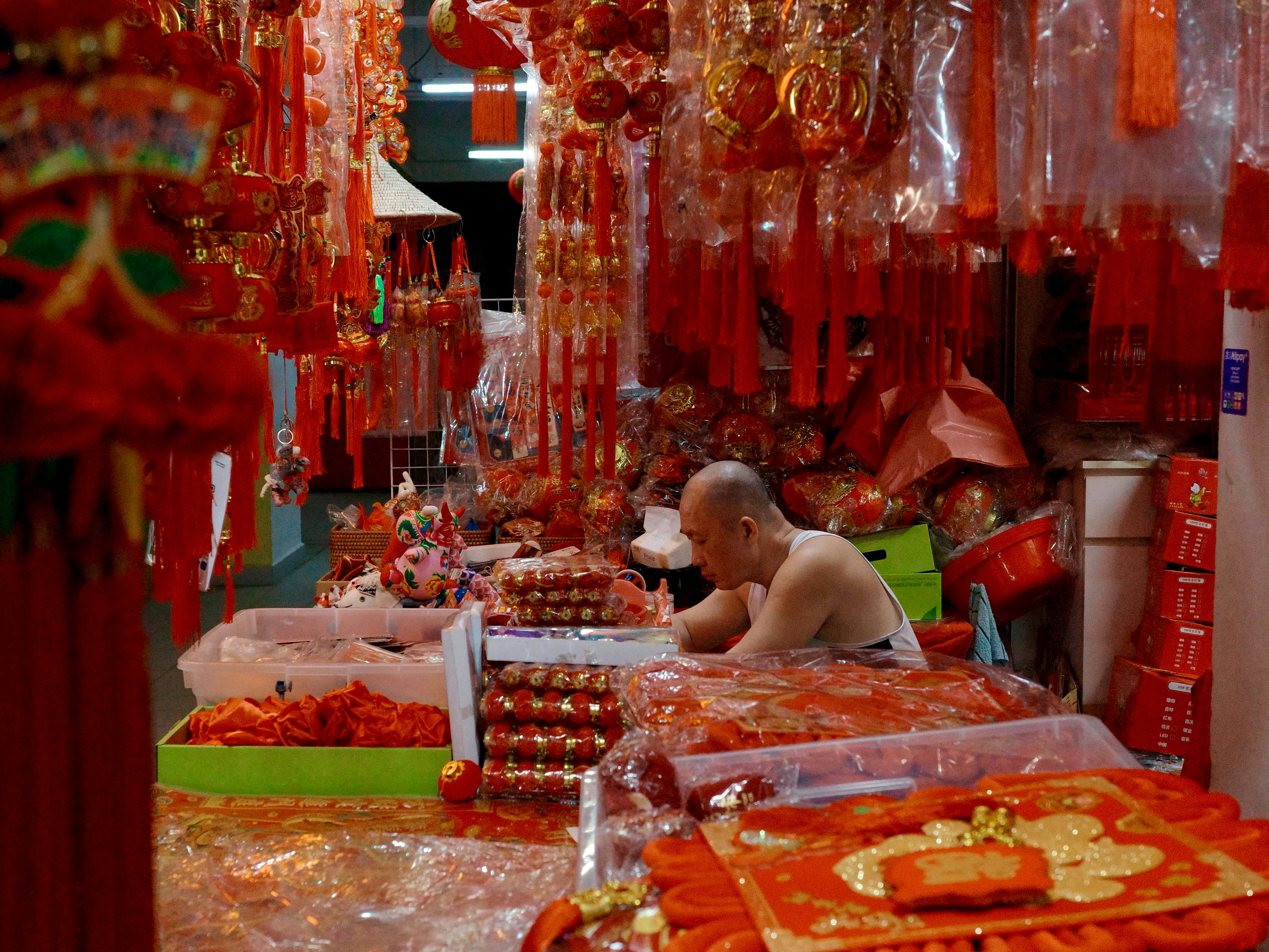 Red Lanterns and Quiet Focus: A Vendor Amidst Golden Market Bounty