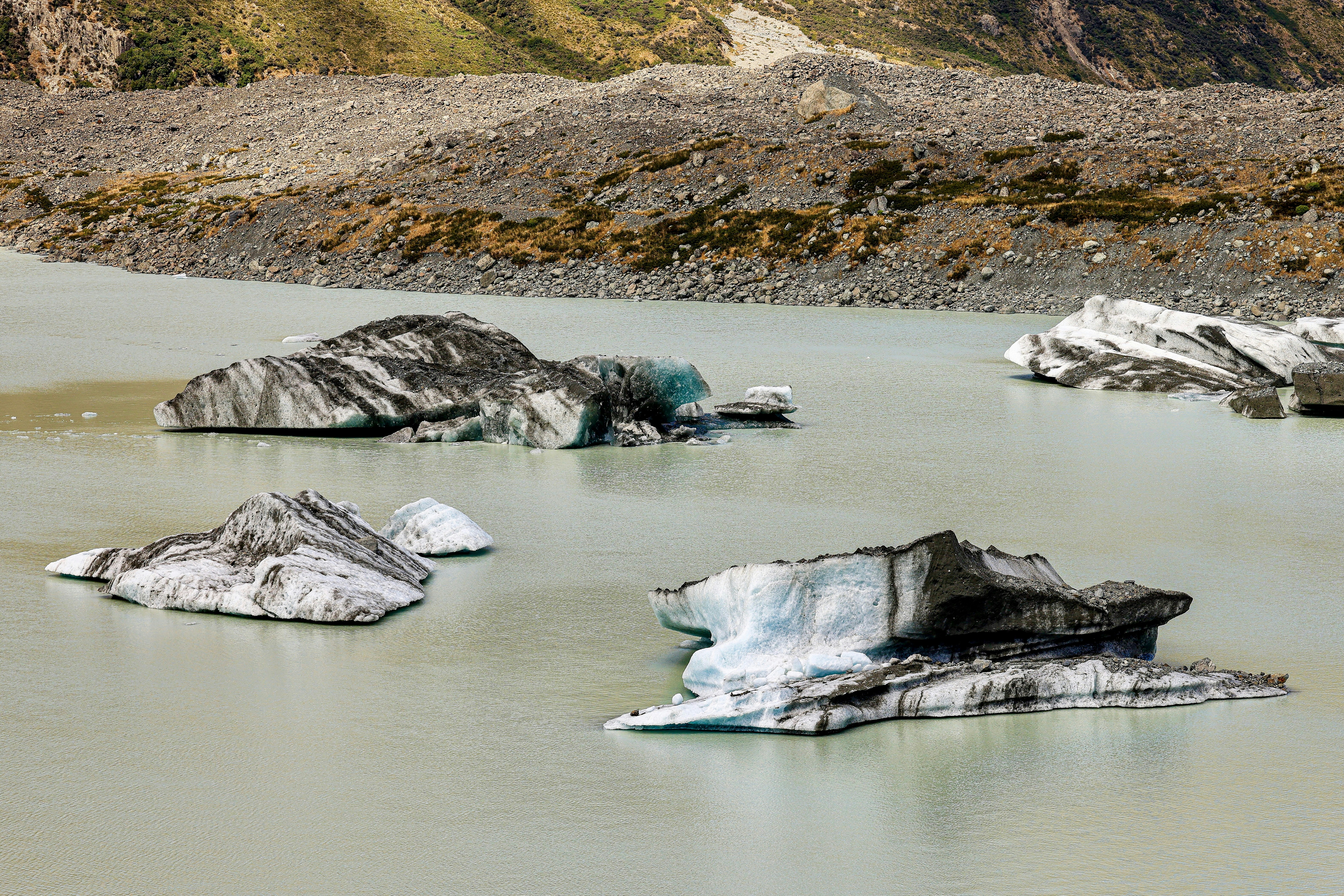 Glacial Boats in Teal Waters: Icebergs Resting under a Rocky Shore